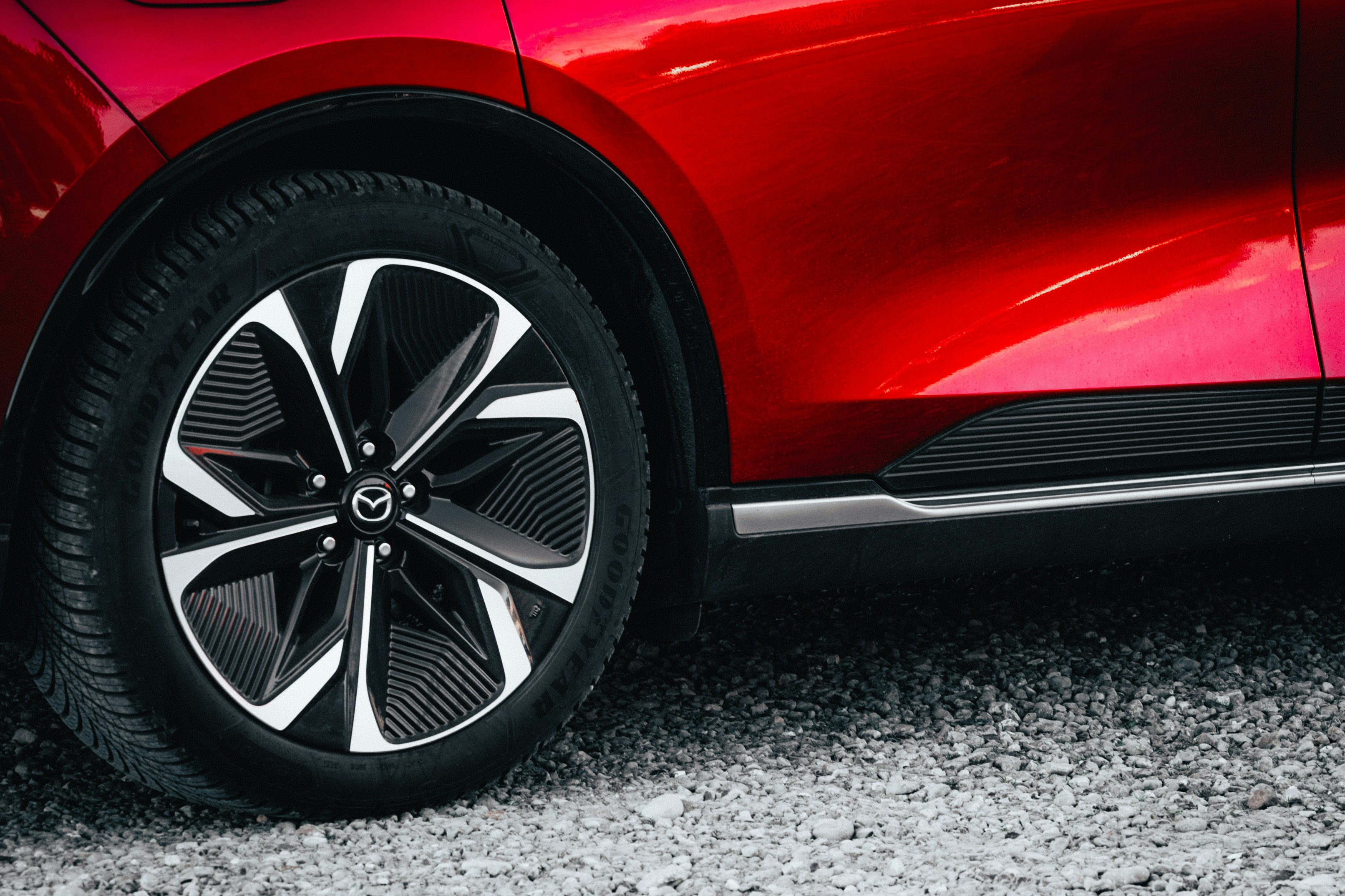 Red Metallic Side Profile: A Mazda rim and lower door blister against a gravel baseline