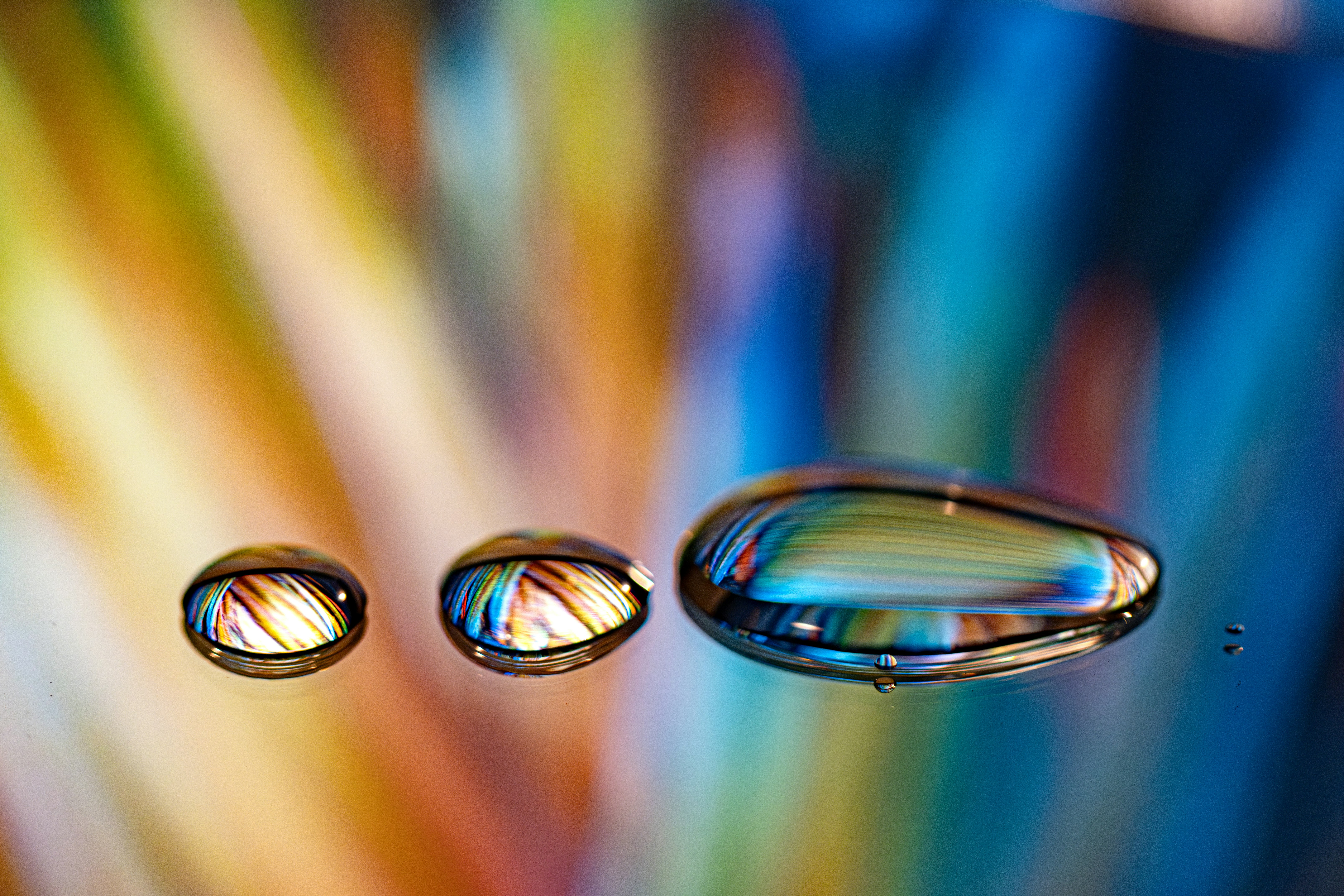 Colorful droplets on a reflective surface create rainbow refractions and soft bokeh, highlighting micro textures and cinematic color separation.