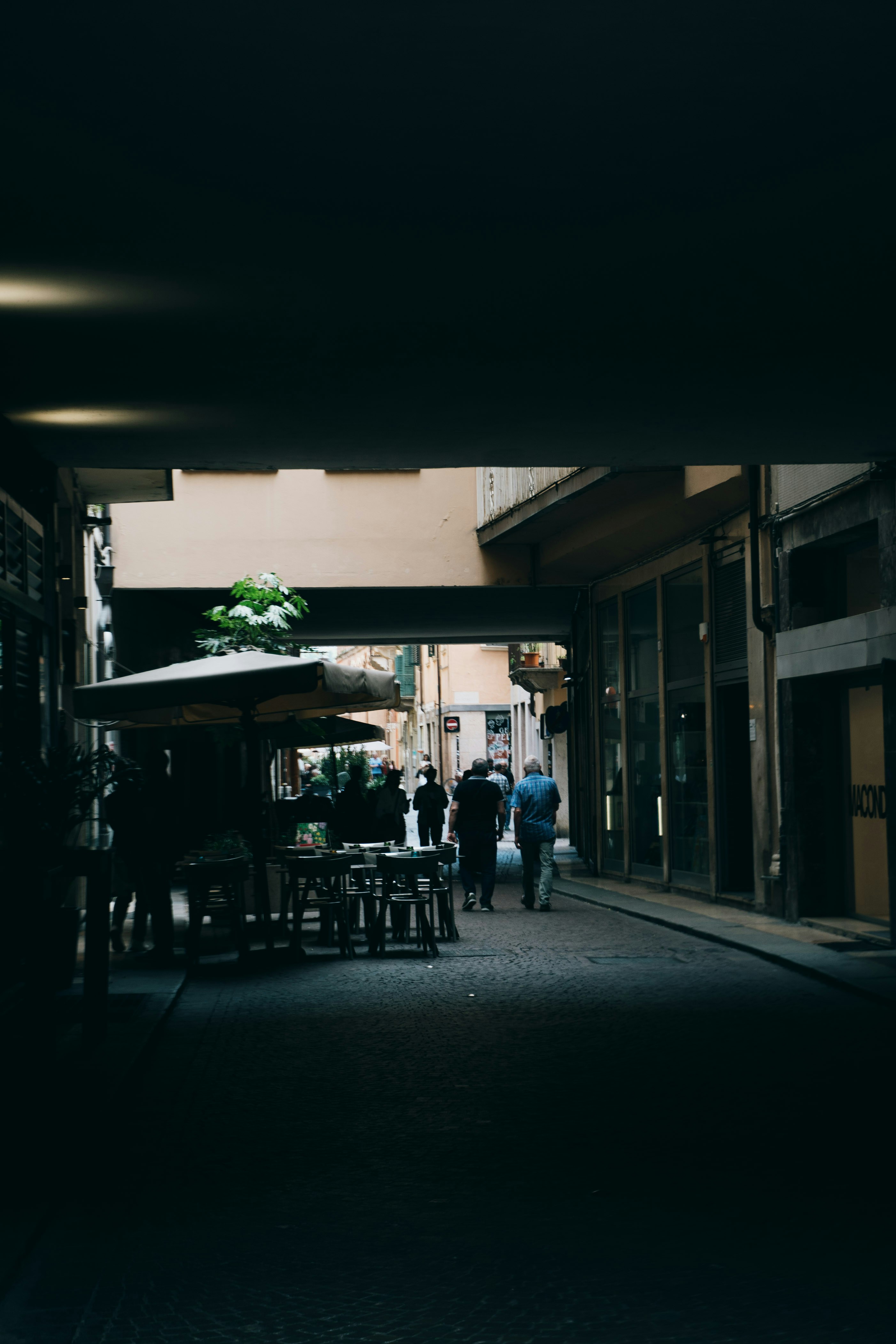  pedestrians in a sunlit alley framed by urban shade