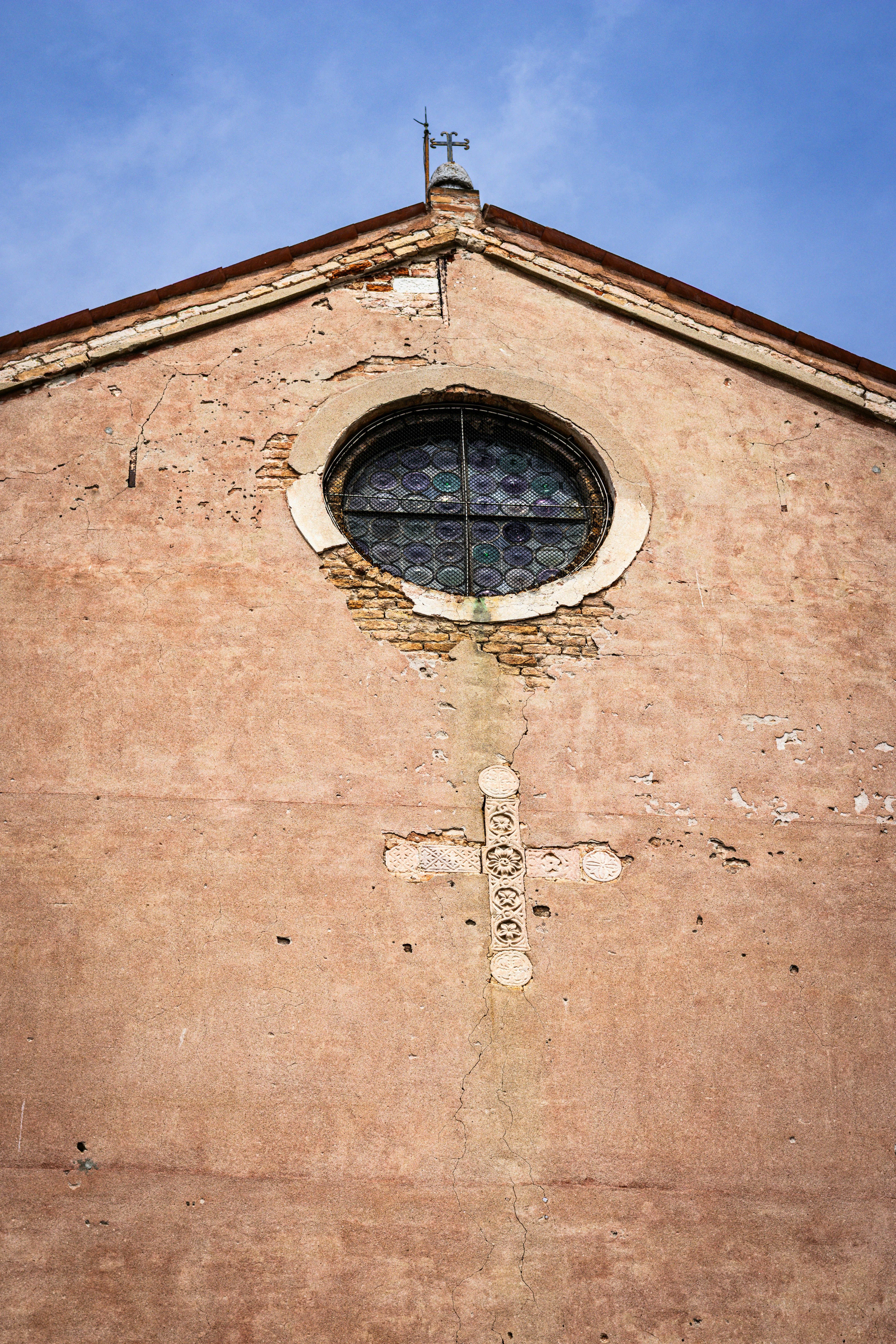 Rose-tinged church wall with circular stained window and weathered cross