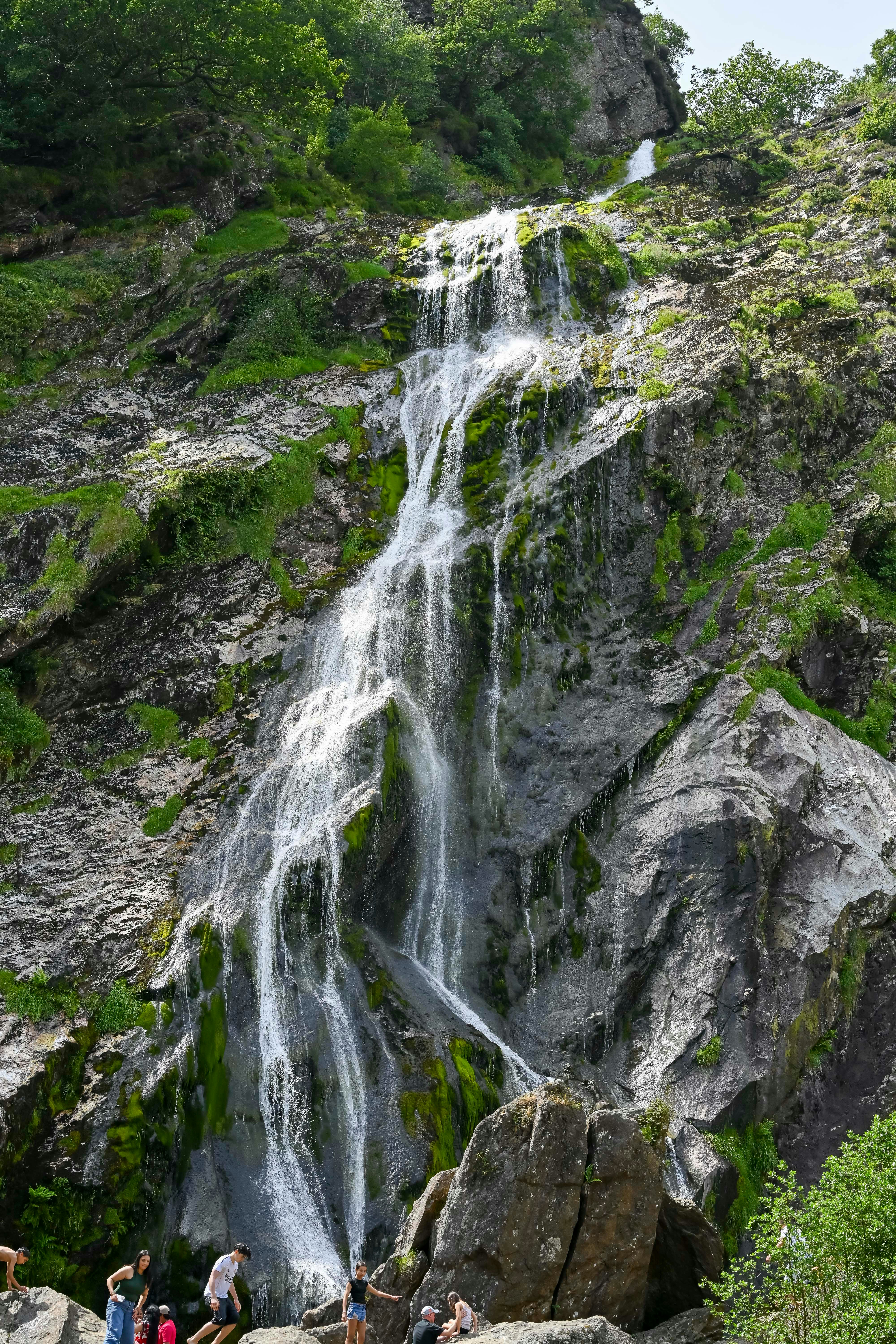 Cascade Over Stone: A Dappled Waterfall amid Rugged Green Cliffs