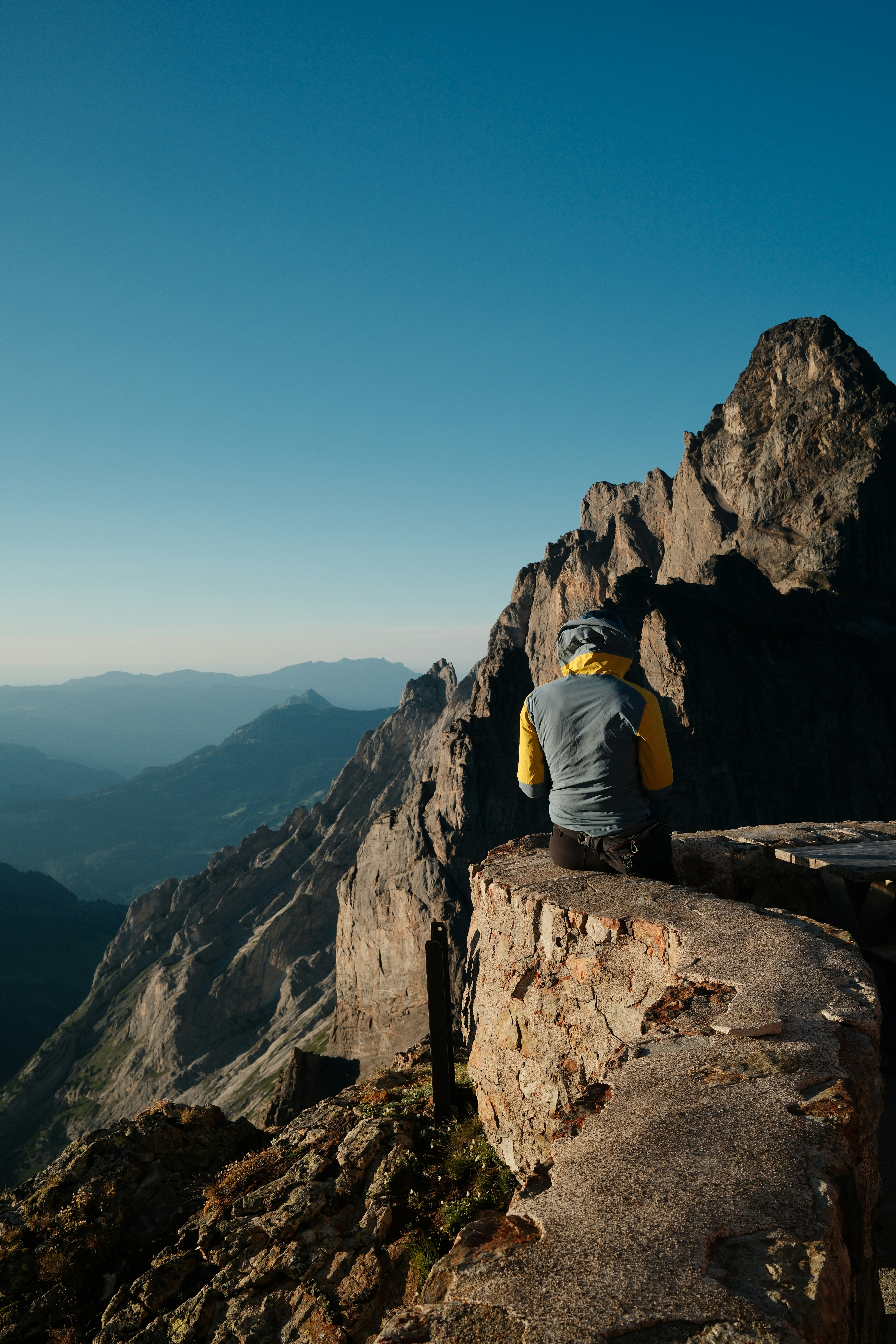 Edge of Silence: climber seated on alpine ledge as sun paints jagged cliff faces