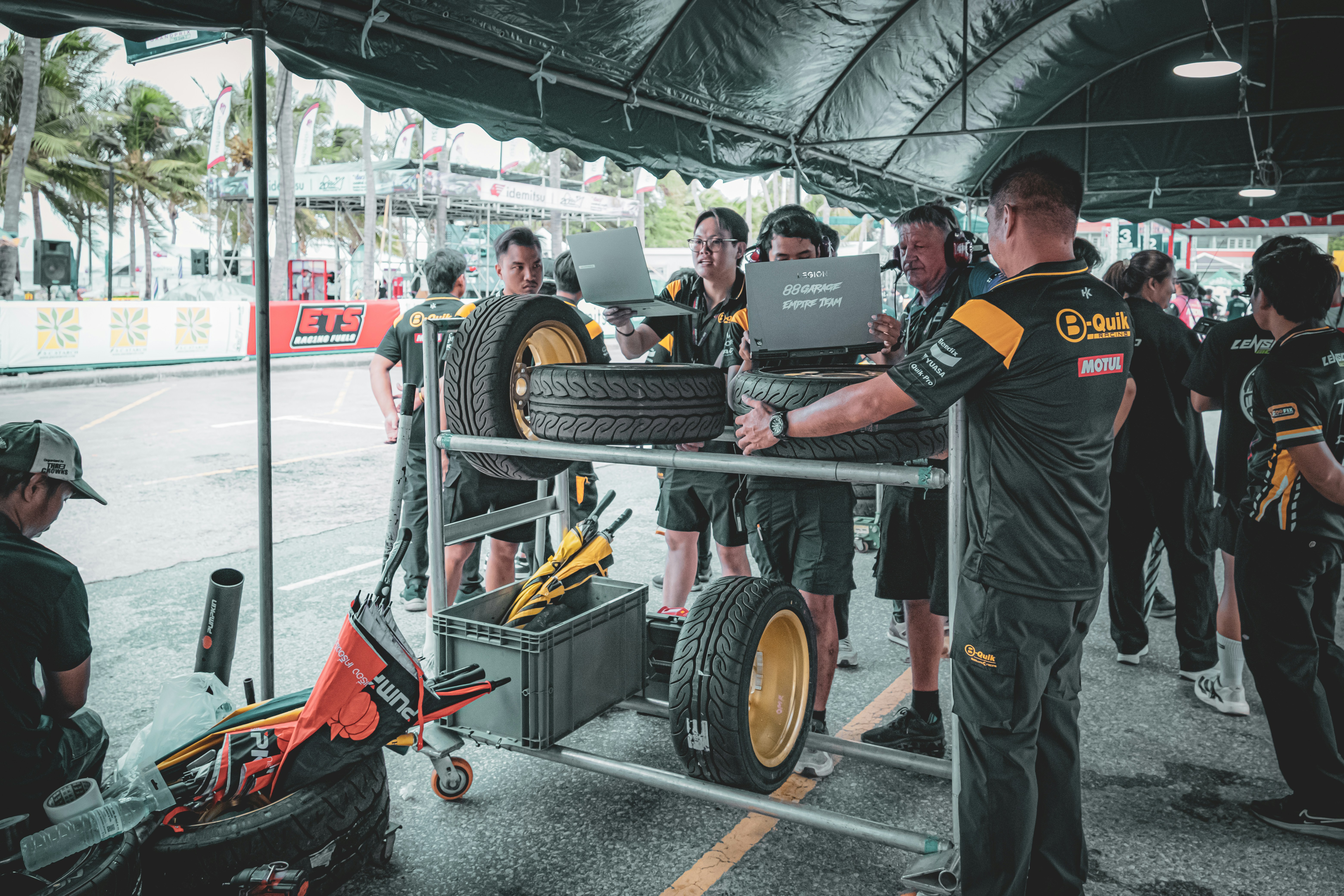 Race engineers and mechanics analyze vehicle data while preparing racing tires during the Porsche Carrera Cup Asia paddock. The image captures the teamwork, engineering, and technical operations behind professional GT motorsport, highlighting race strategy, telemetry analysis, and tire preparation before competition