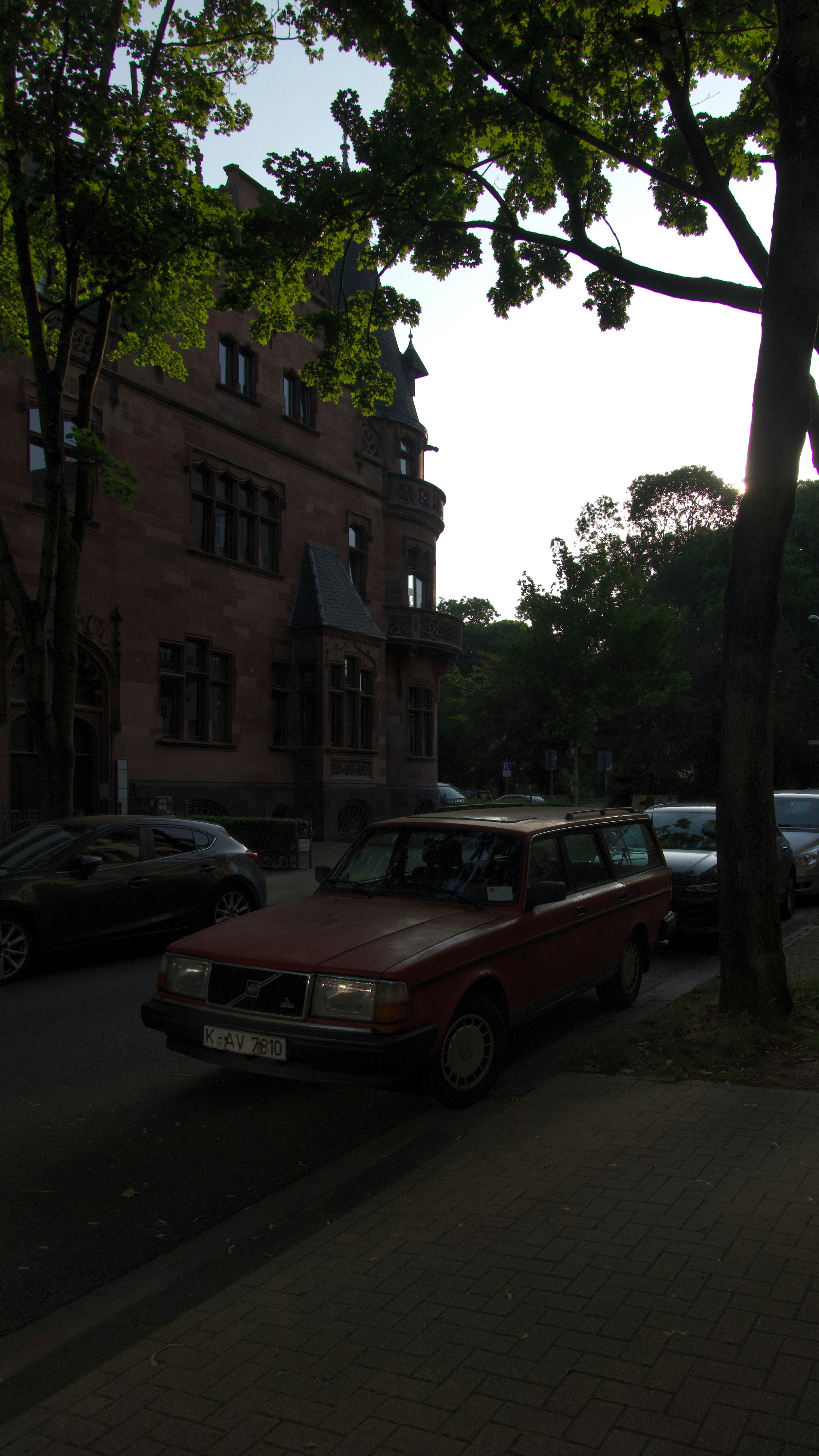 Red Volvo on a Quiet City Street Framed by Gnarled Trees and a Historic Building