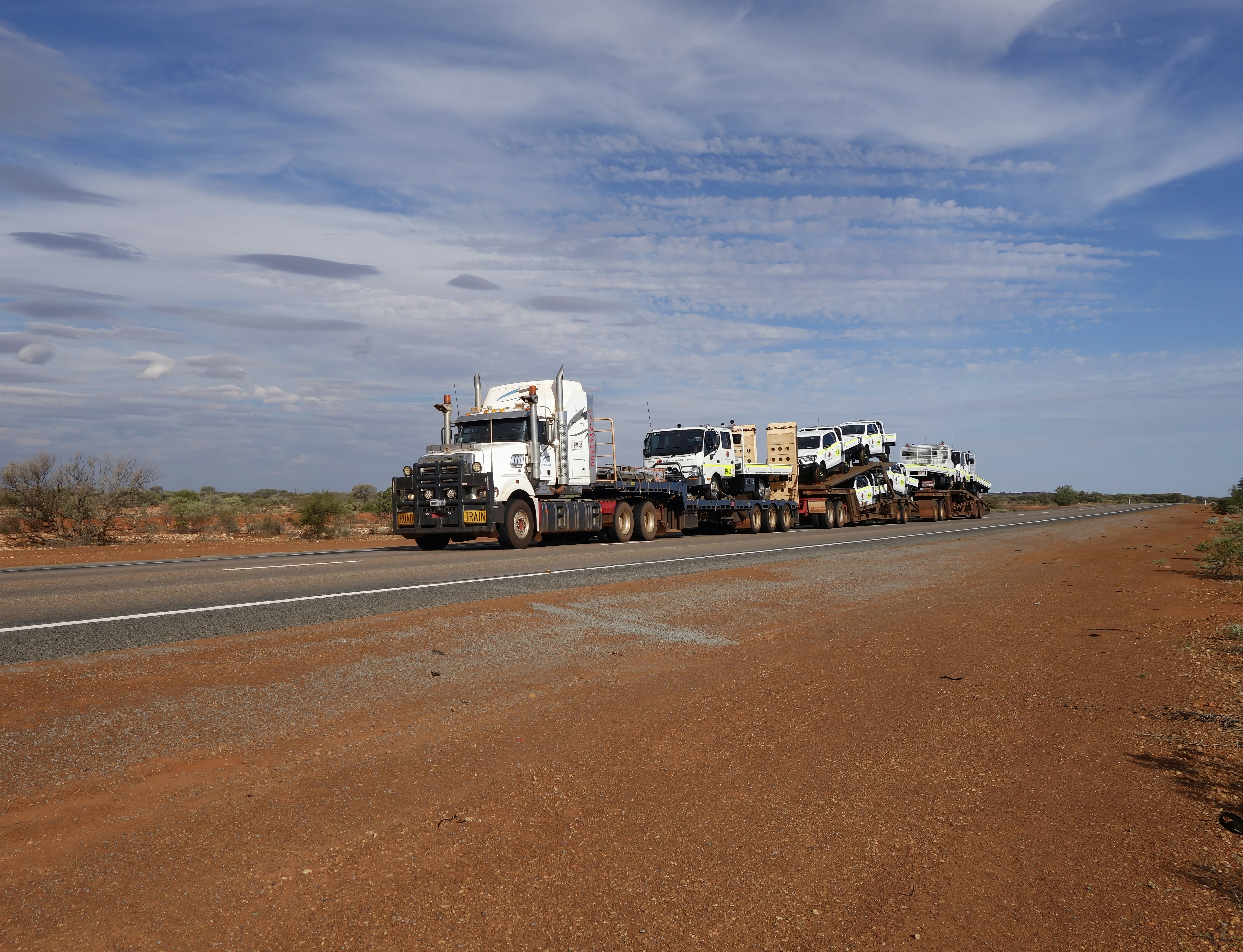 A road train carrying trucks on a red dirt road.