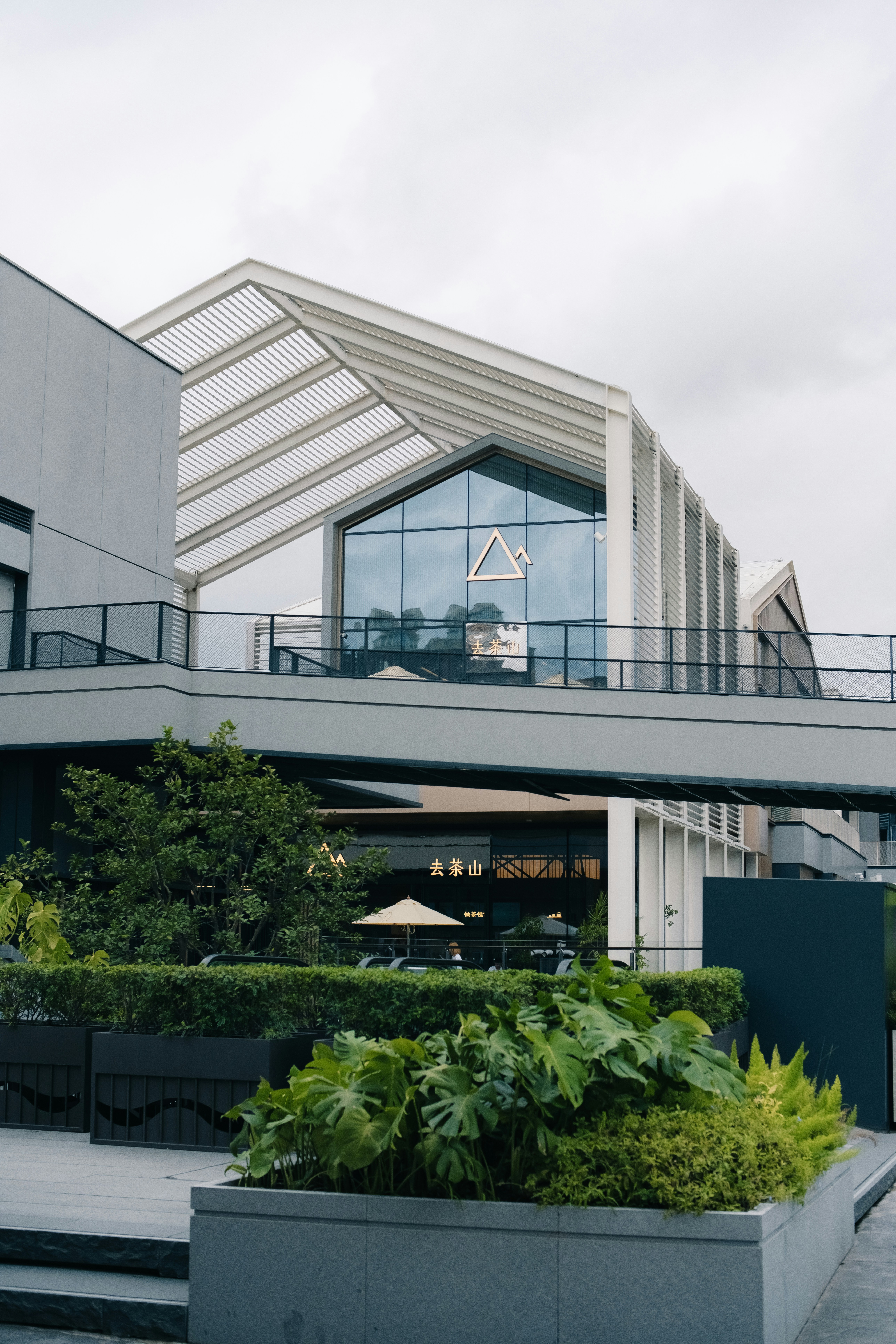 Sleek, angular glass architecture sits above urban greenery, with a pedestrian bridge weaving through a contemporary complex.