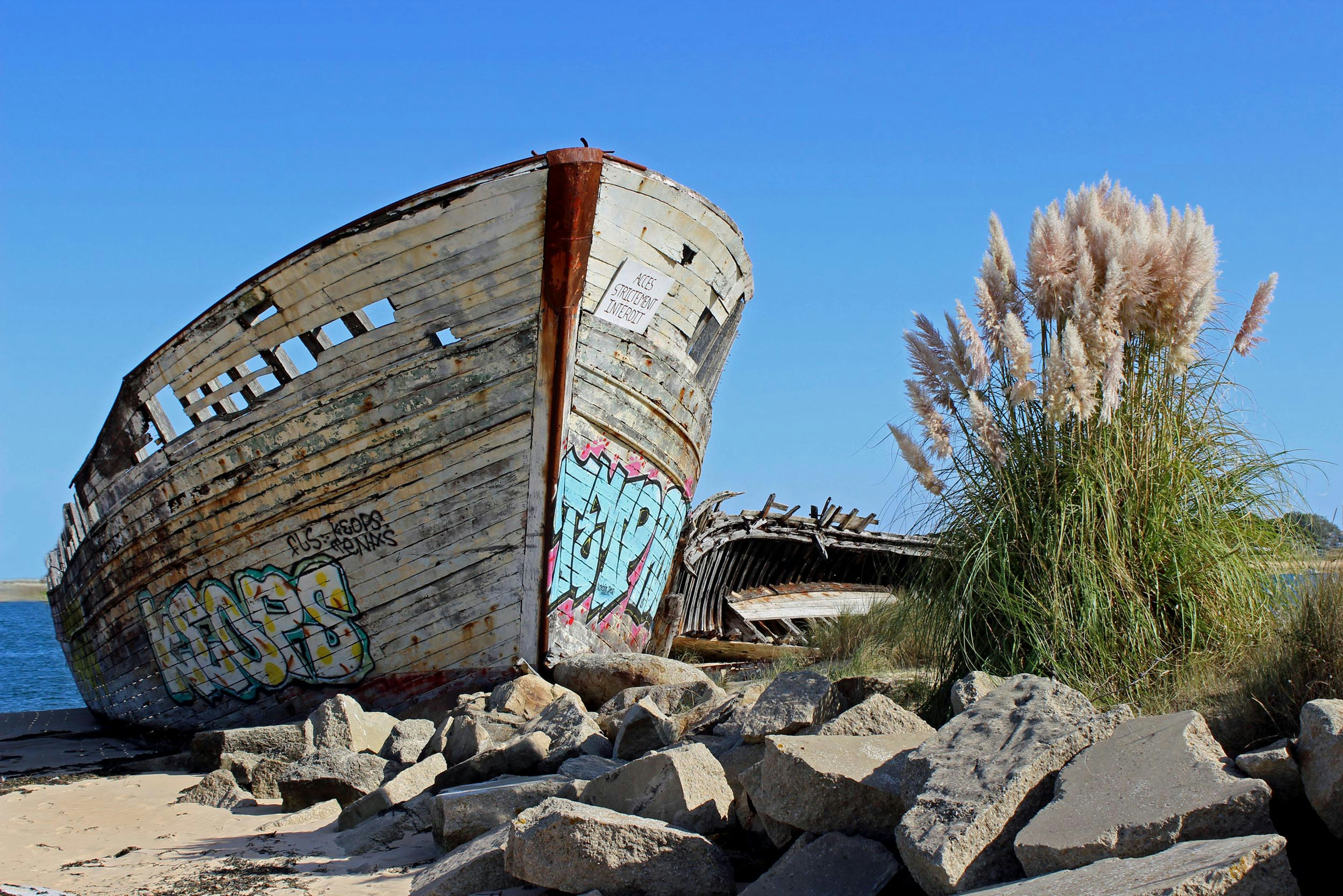 Abandoned hull adrift on a rocky shoreline under a crisp blue sky