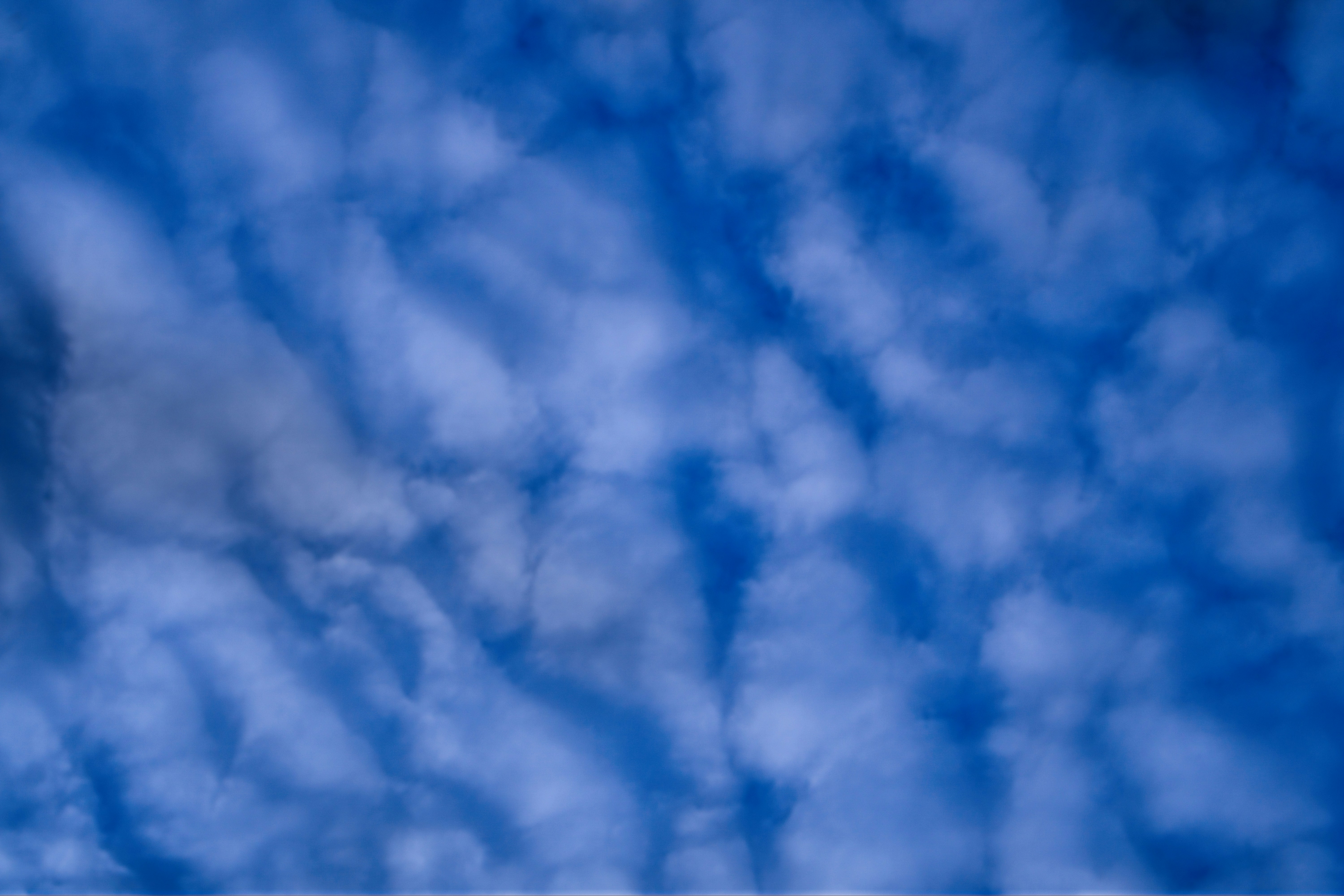 Dense blue sky with textured white clouds forming a soft pattern for an expansive aerial mood.