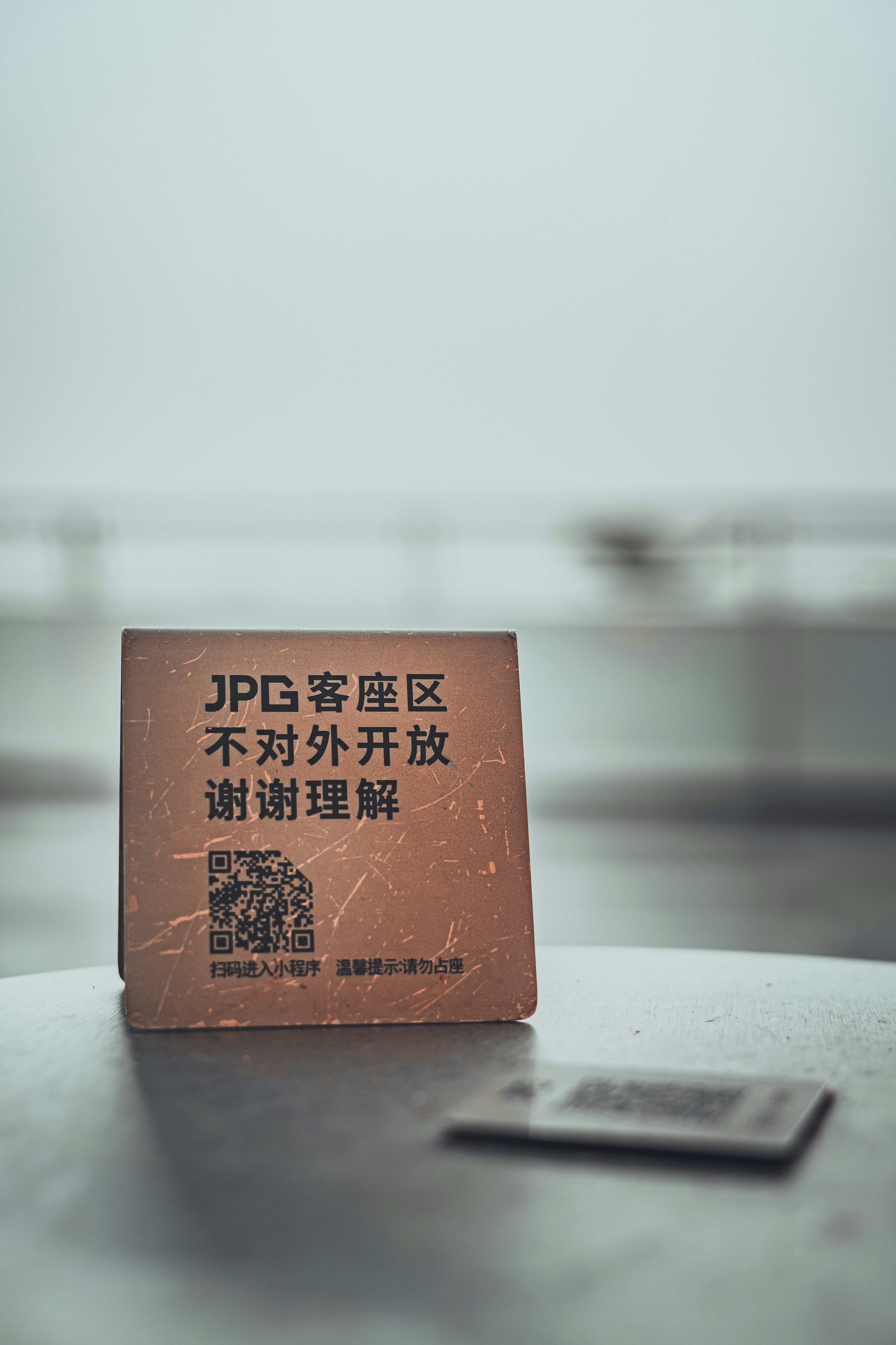 A brown card with Chinese text and a QR code sits on a smooth surface, with a blurred background and a separate card lying nearby; the scene appears to be a still life in a softly lit indoor setting.