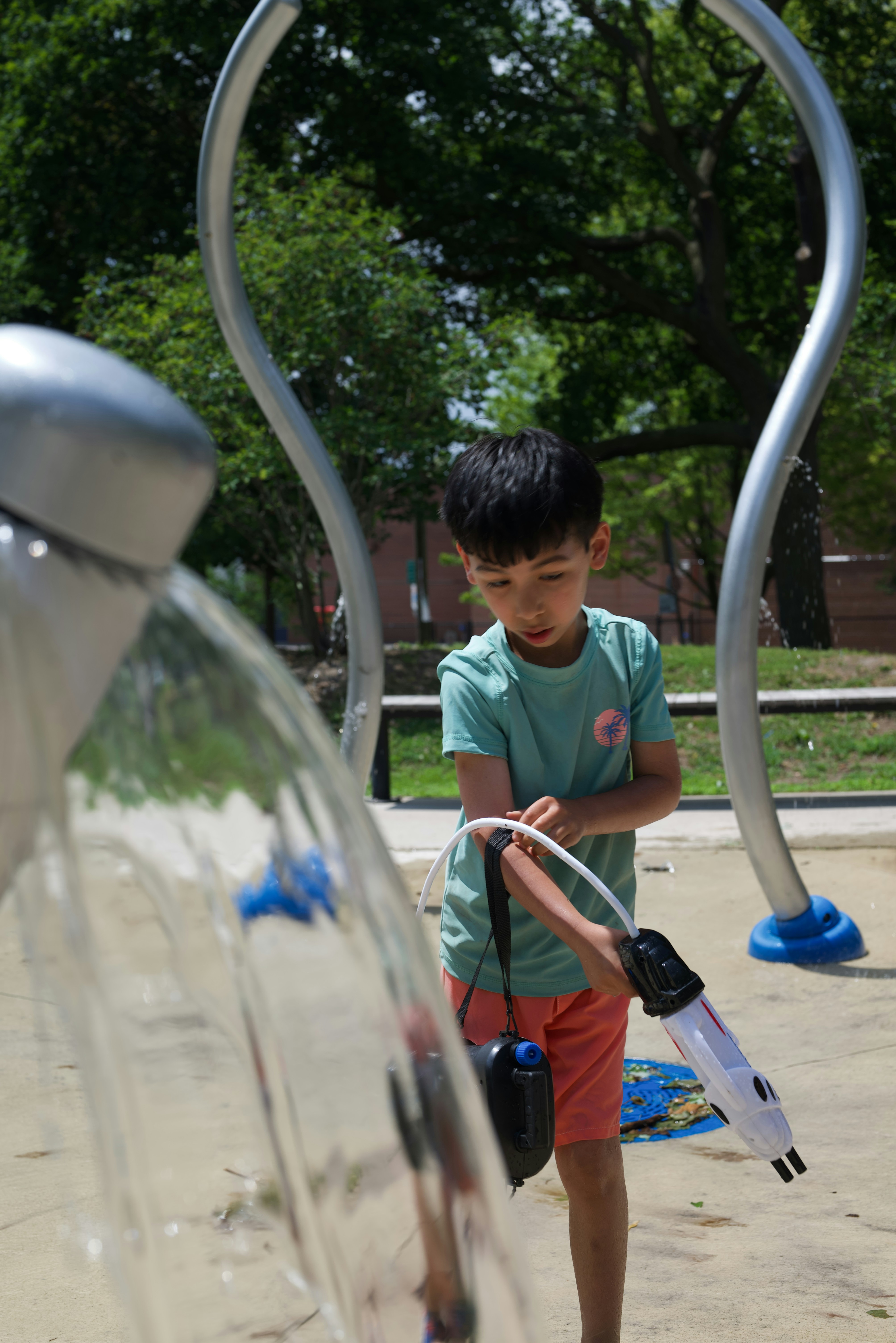 Boy in turquoise shirt with toy blaster under looping playground frame