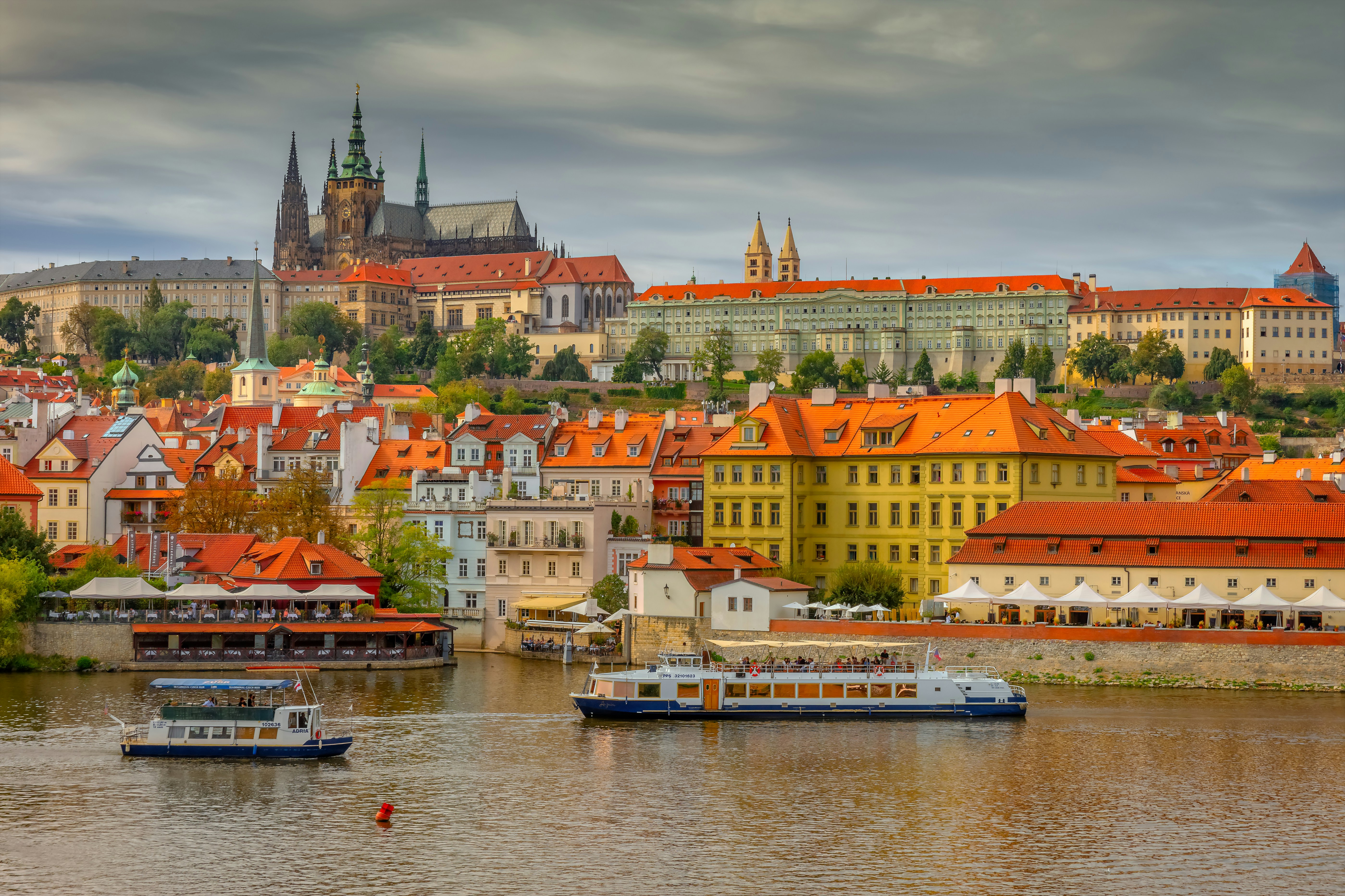 Riverside Prague: Boats Skim Along Vltava Beneath Historic Red-Tiled Rooftops