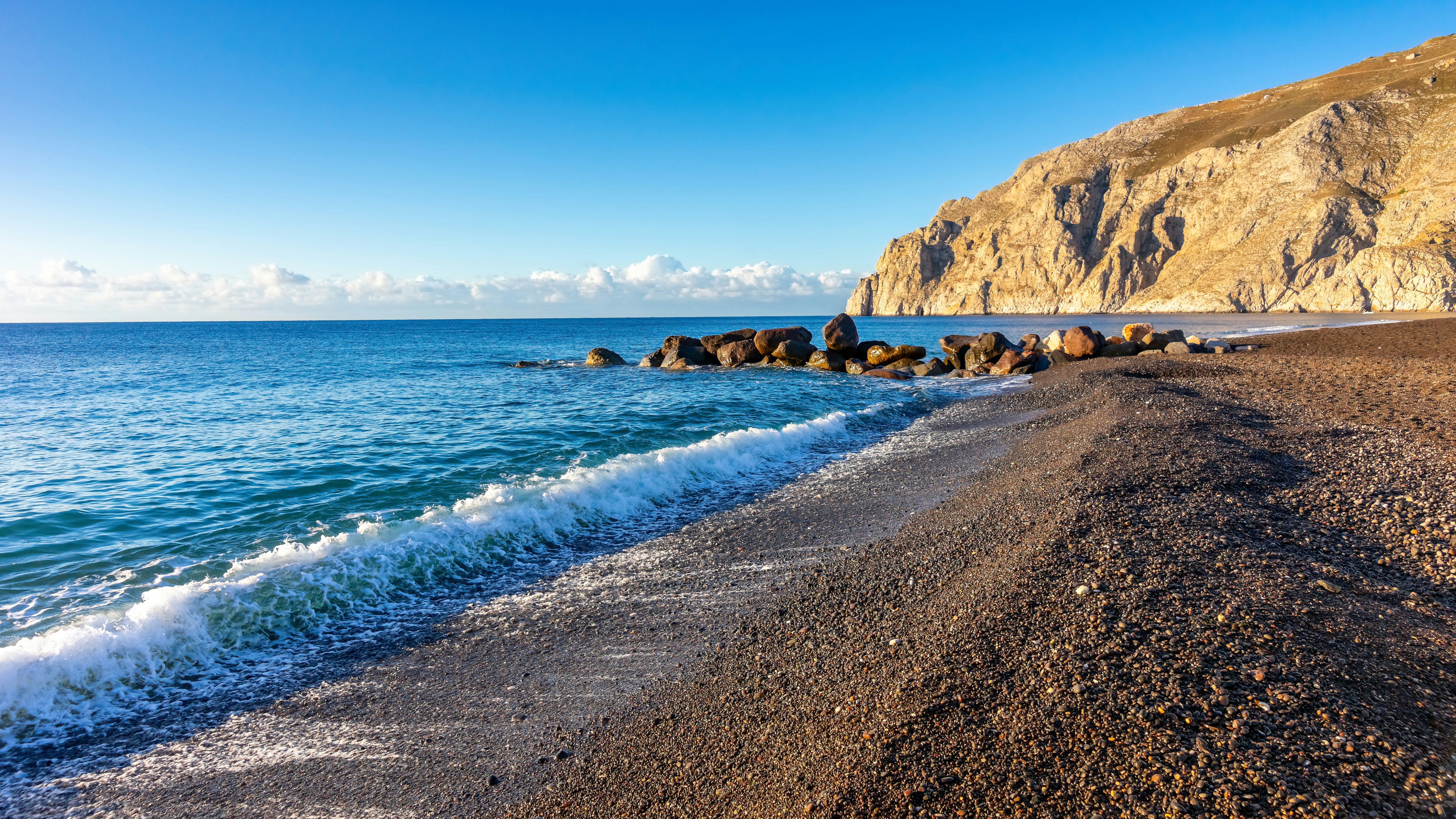 Coastal Cliffs Meet Calm Seaside: A Sunlit Beach at Distant Foothills