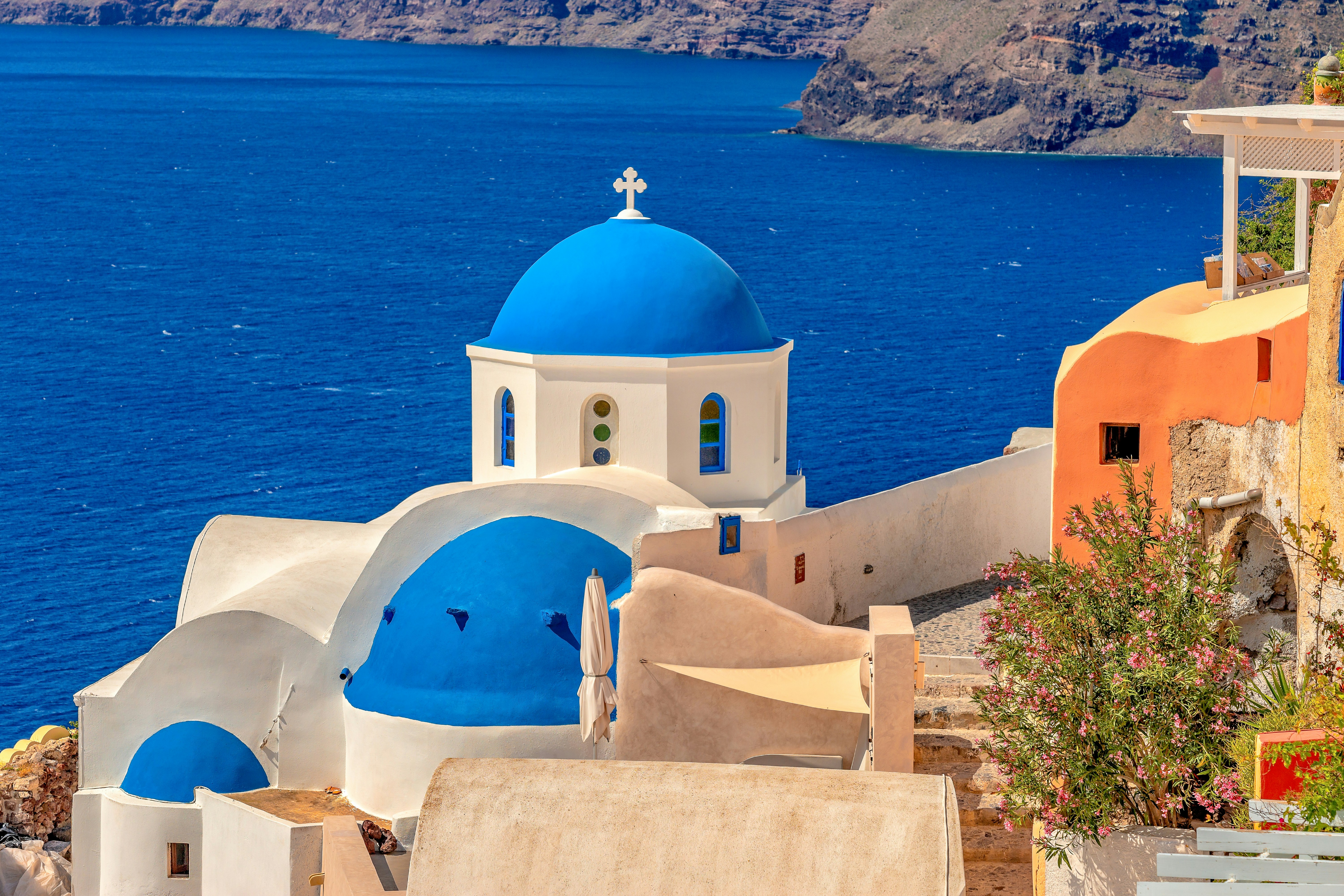 Whitewashed architecture with blue domes against the deep blue sea; a Santorini scene featuring iconic churches and sunlit terraces.