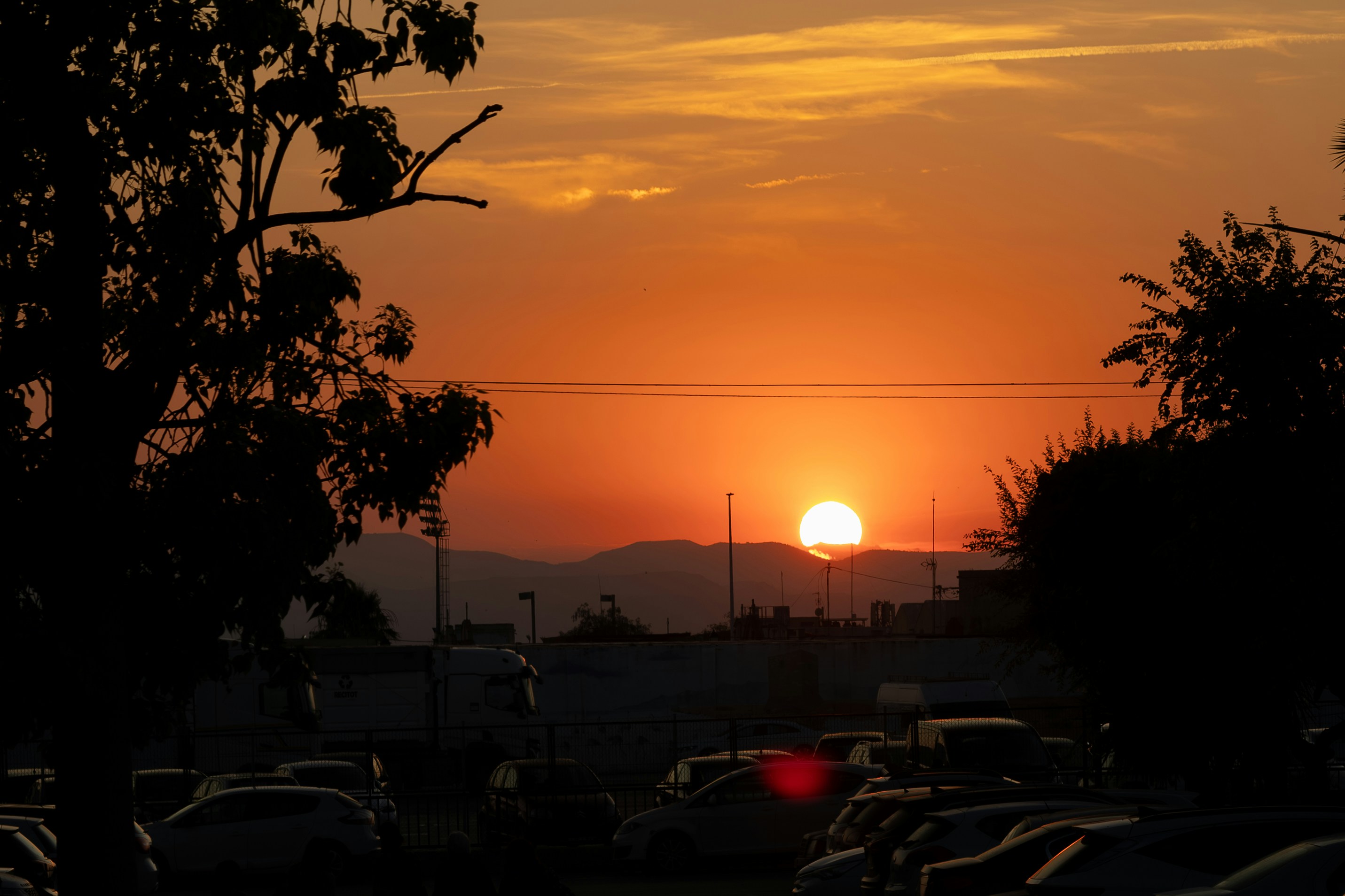Sunset Core: The Sun dipping behind a silhouette of trees and parked cars