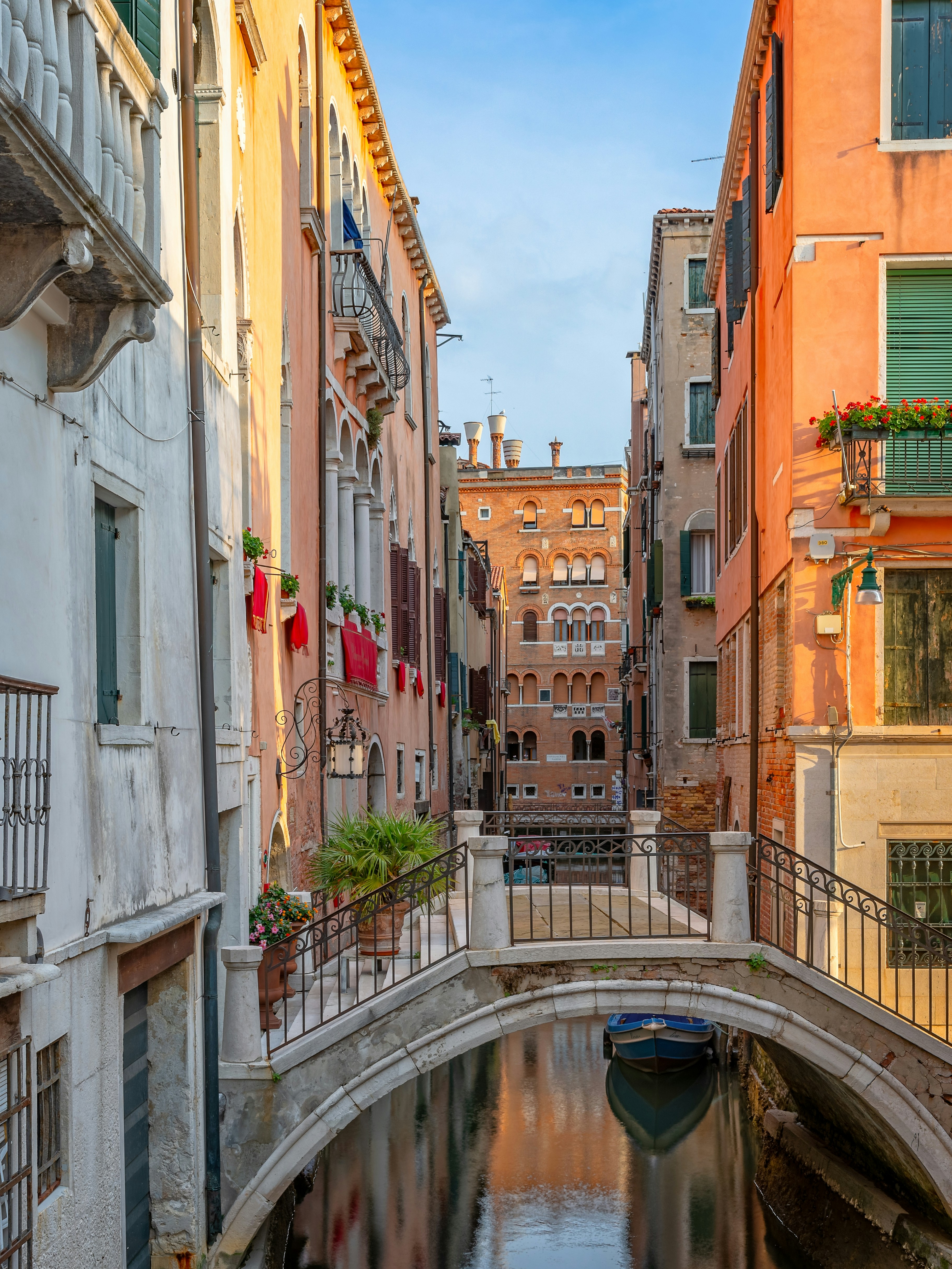 Colorful canal passage: sunlit Venetian-style street arching over a quiet canal