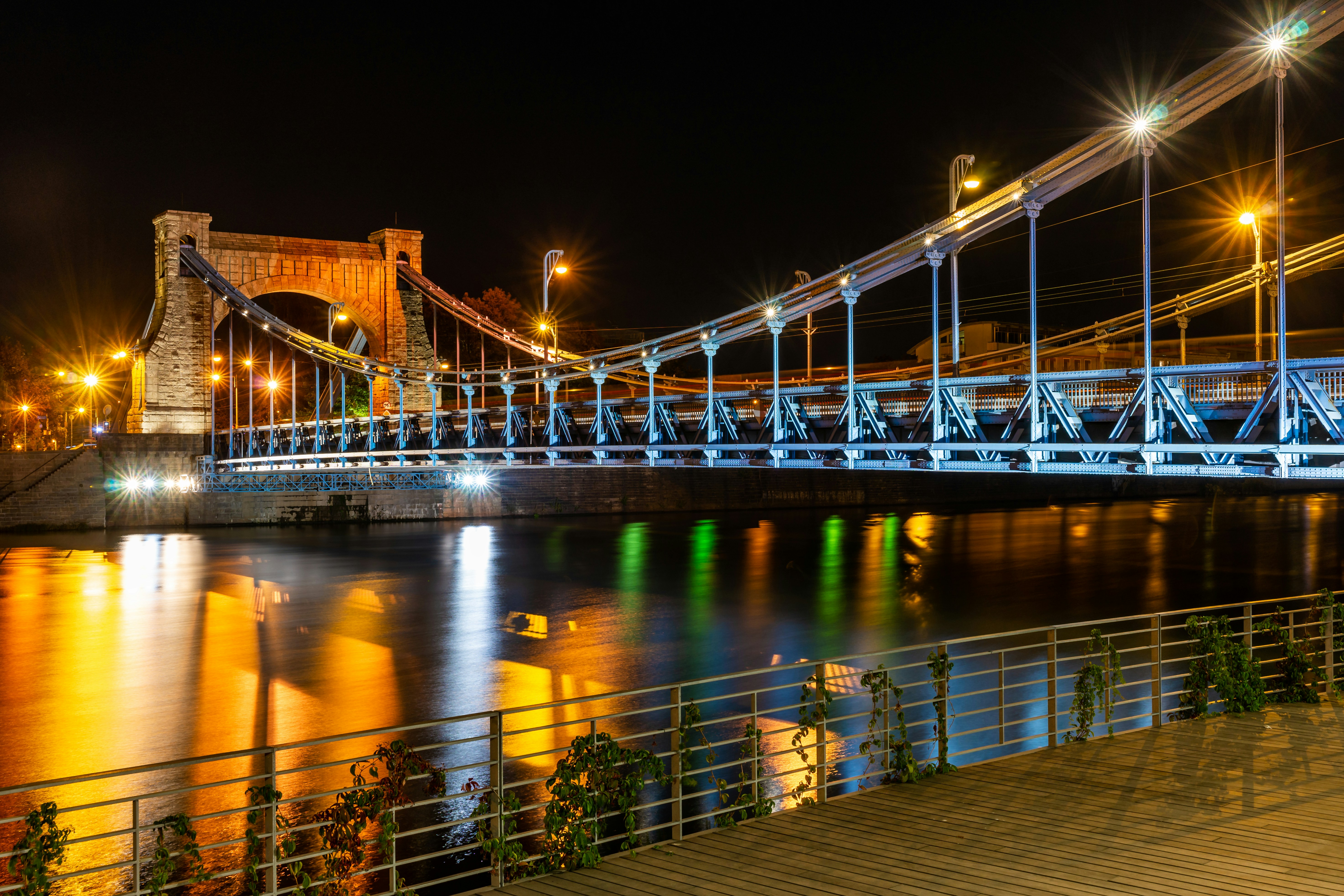 Illuminated Suspension Bridge Over Quiet River at Night