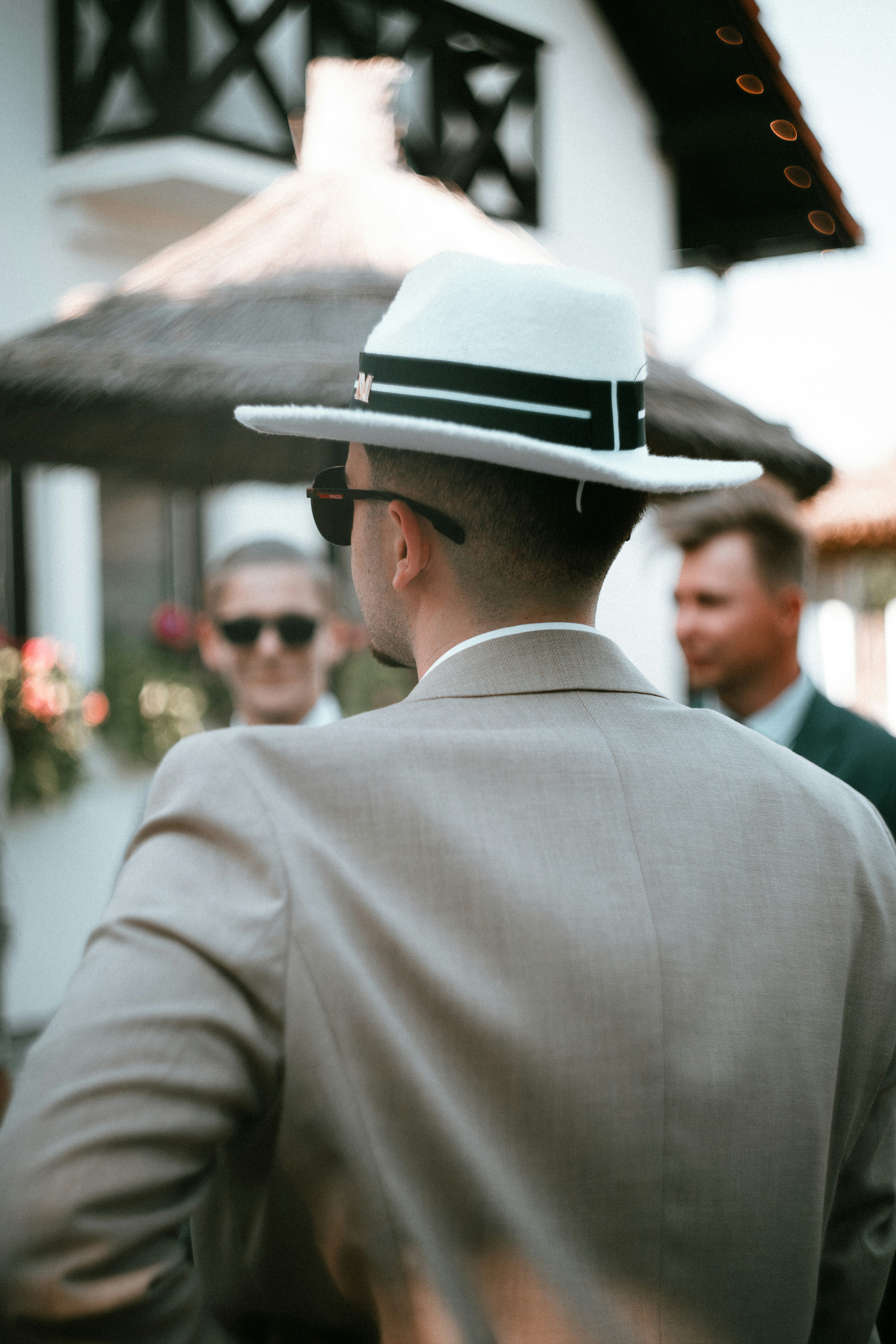 Neutral Palms and Wide Brim: A Gentleman in a Light Fedora at a Courtyard Gathering