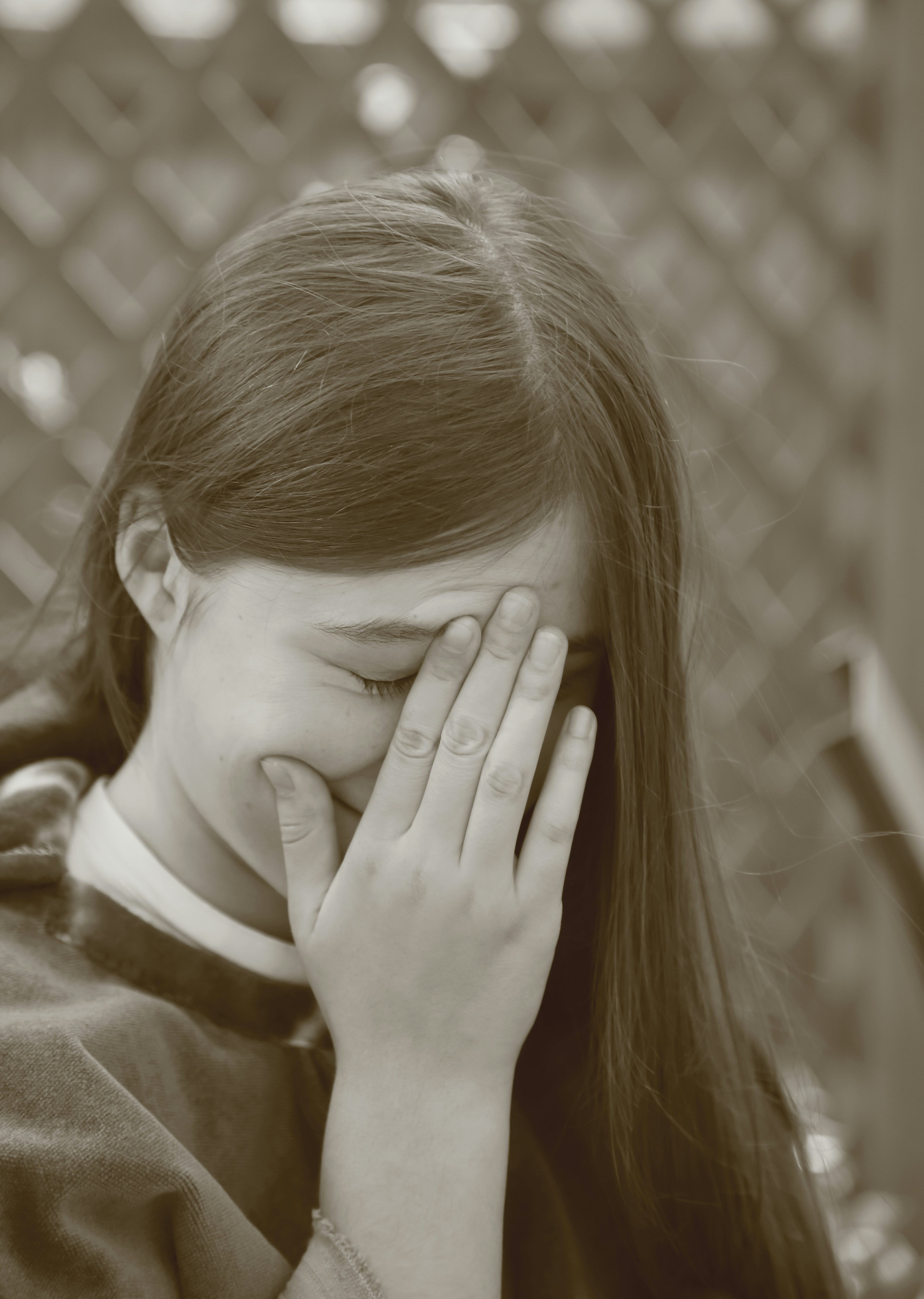 Young girl covers her face with her hand in a candid, intimate moment, captured in sepia tones to emphasize mood and emotion.
