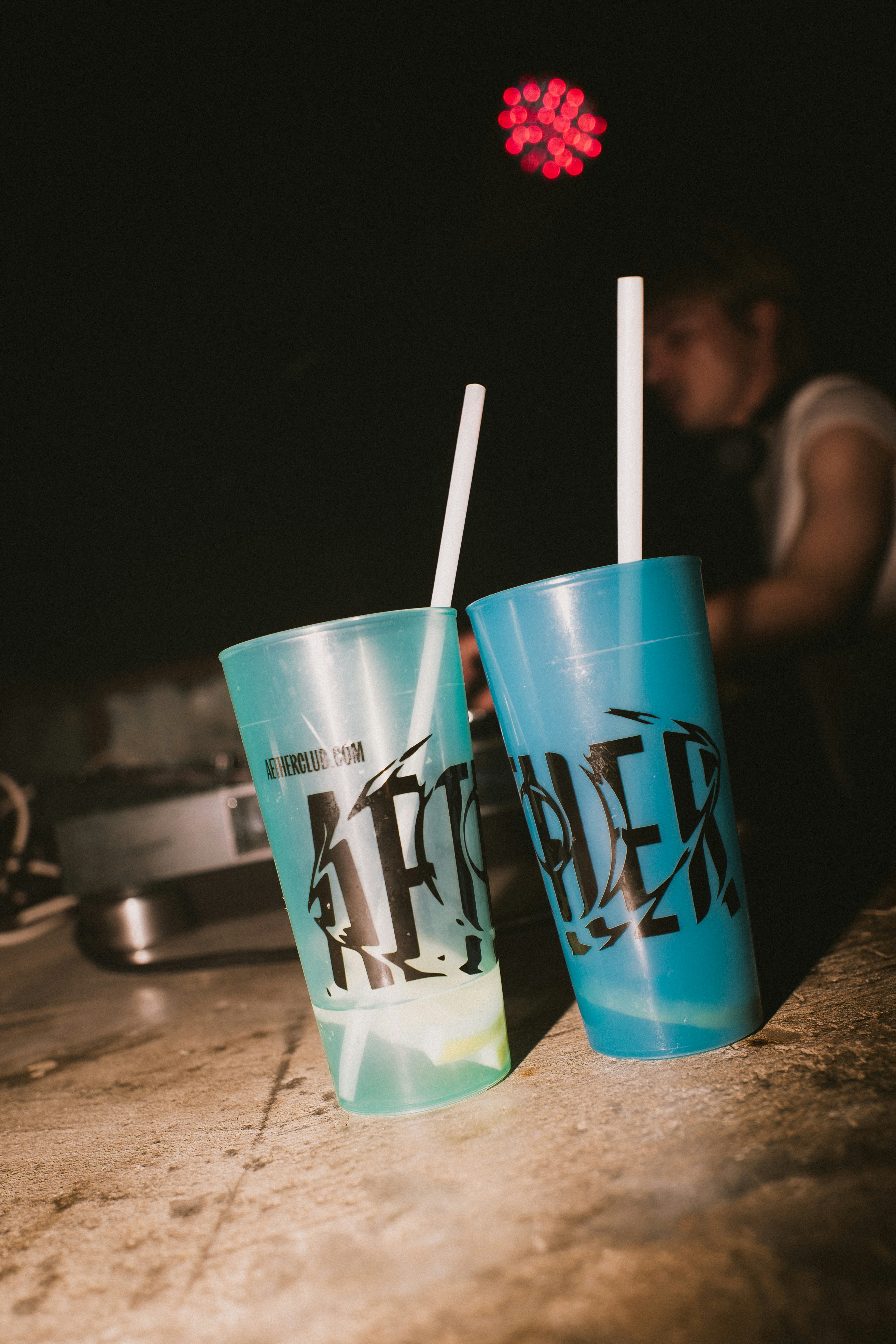Two neon cups leaning on a gritty arcade table at night