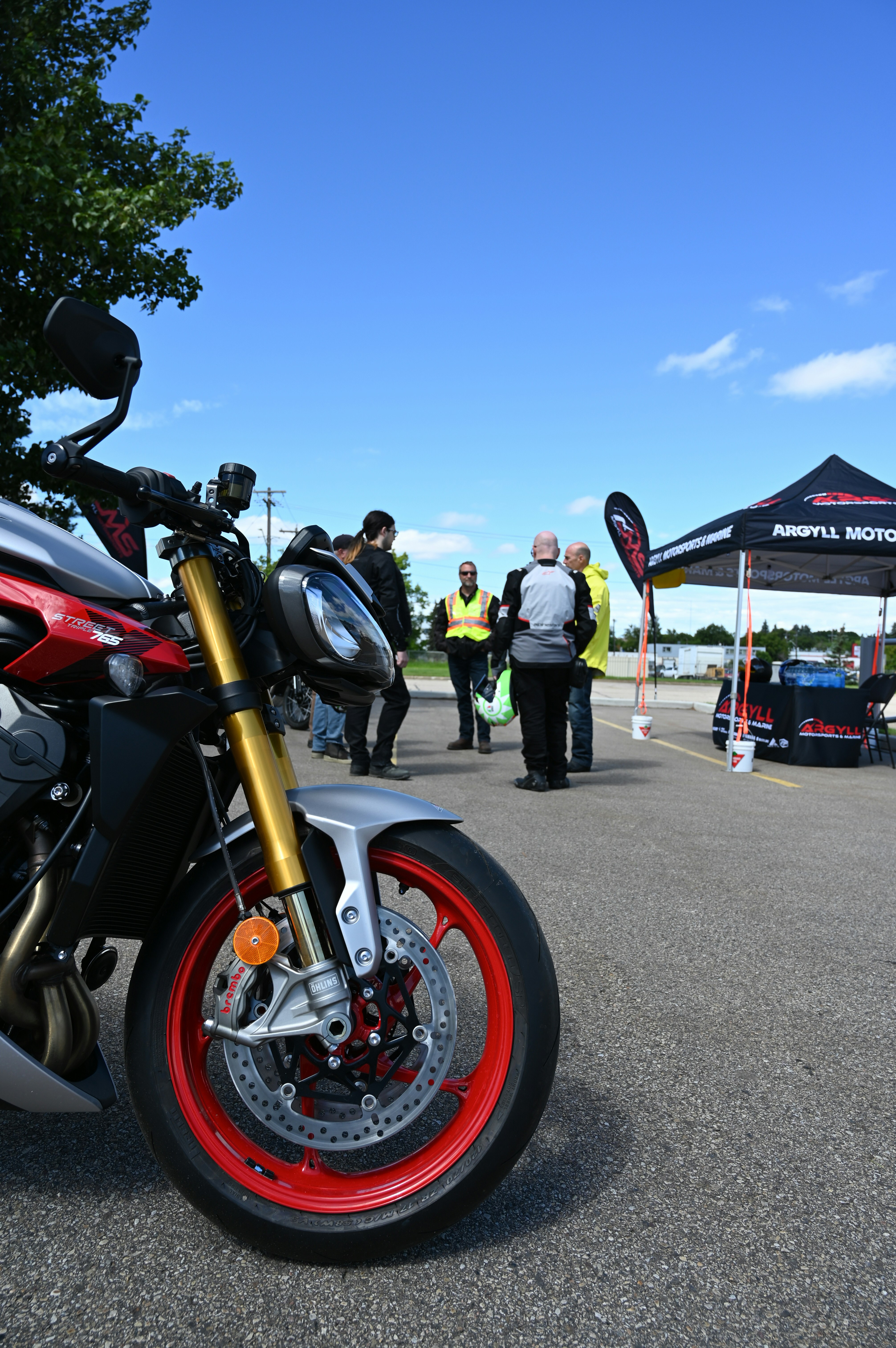 Red-wheeled motorcycle at a gathering under a bright blue sky
