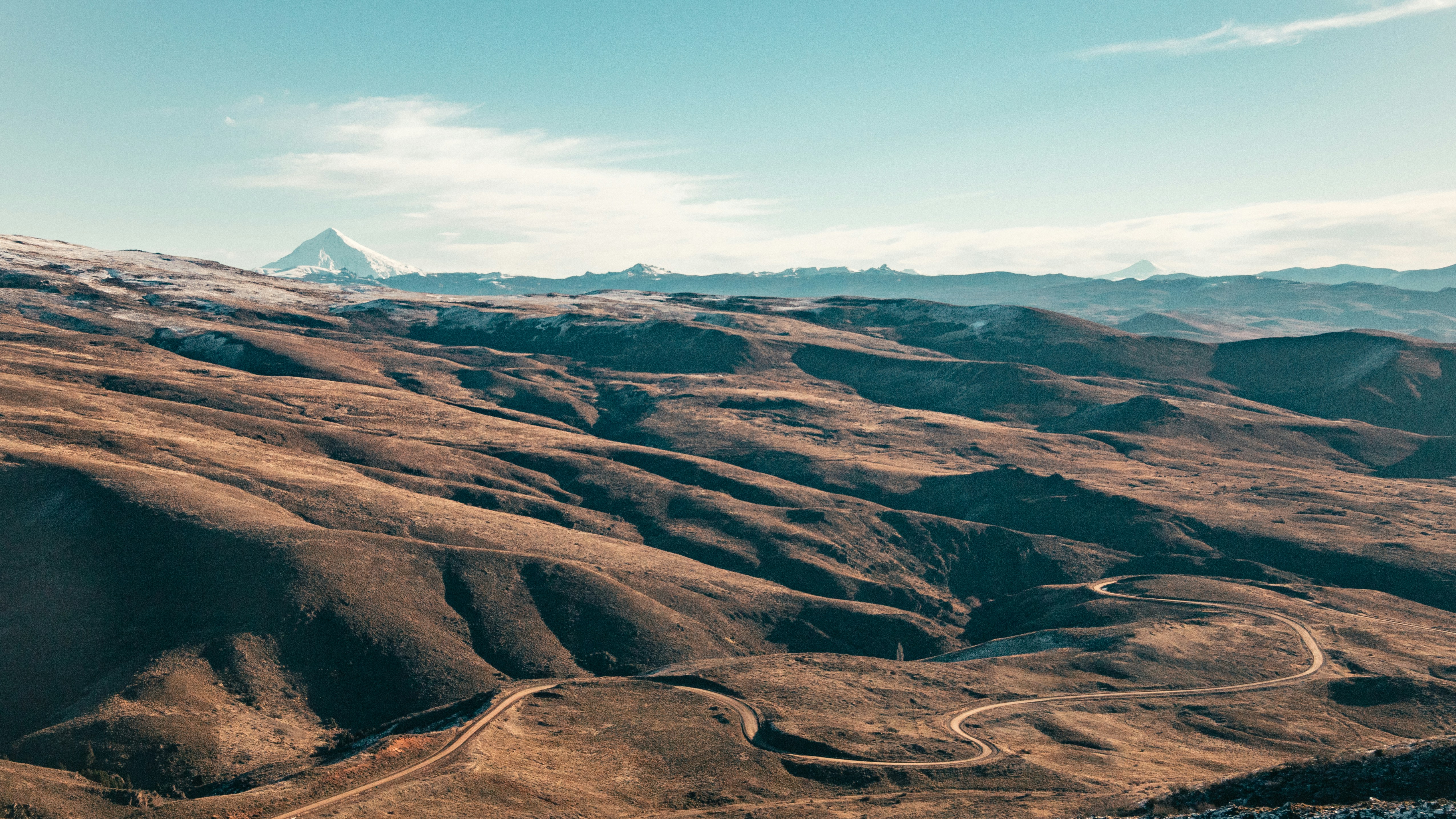 Winding ridges under a pale blue sky near distant snow peaks