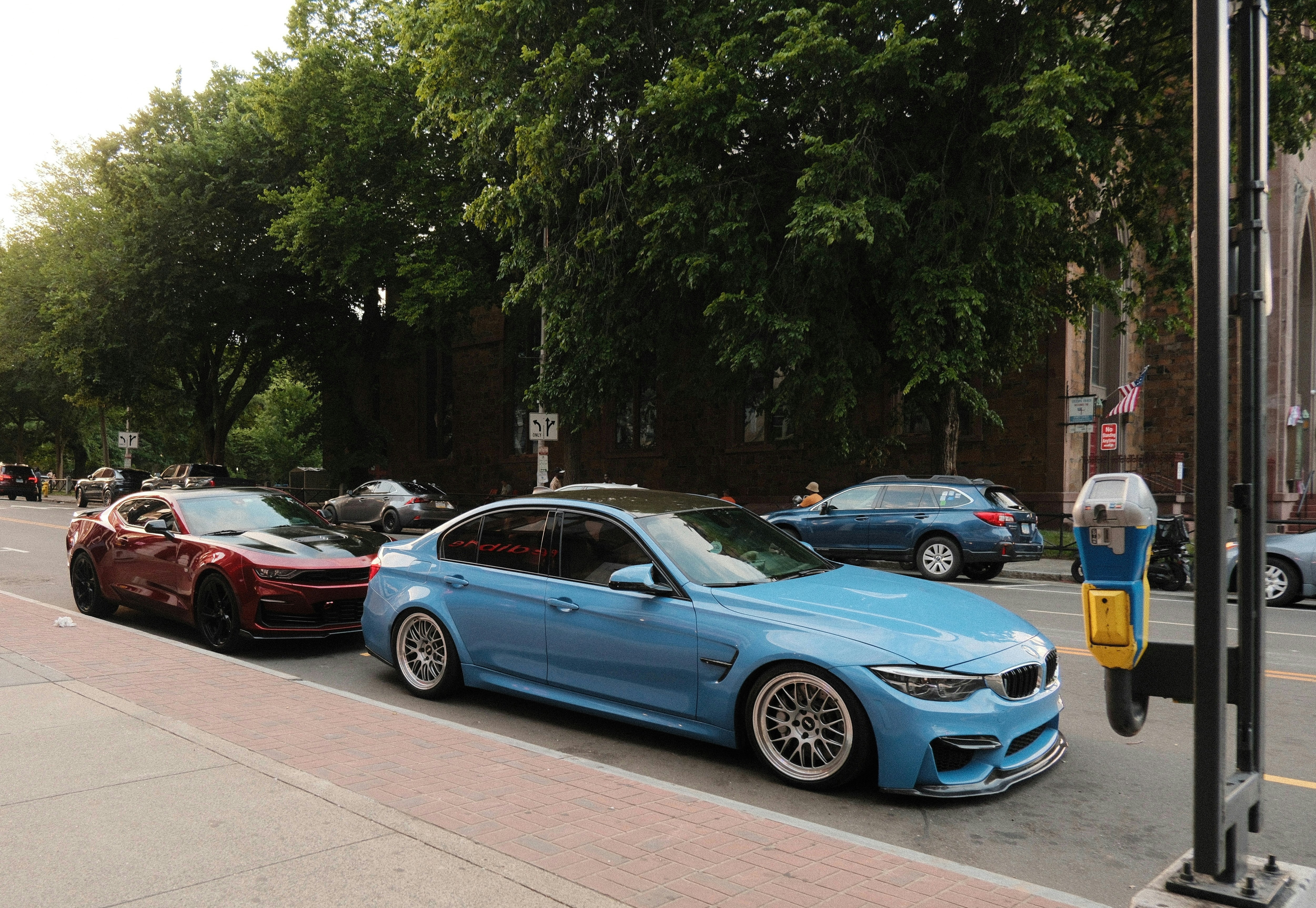Blue BMW sedan parked on a city street with other vehicles and a parking meter in the frame.