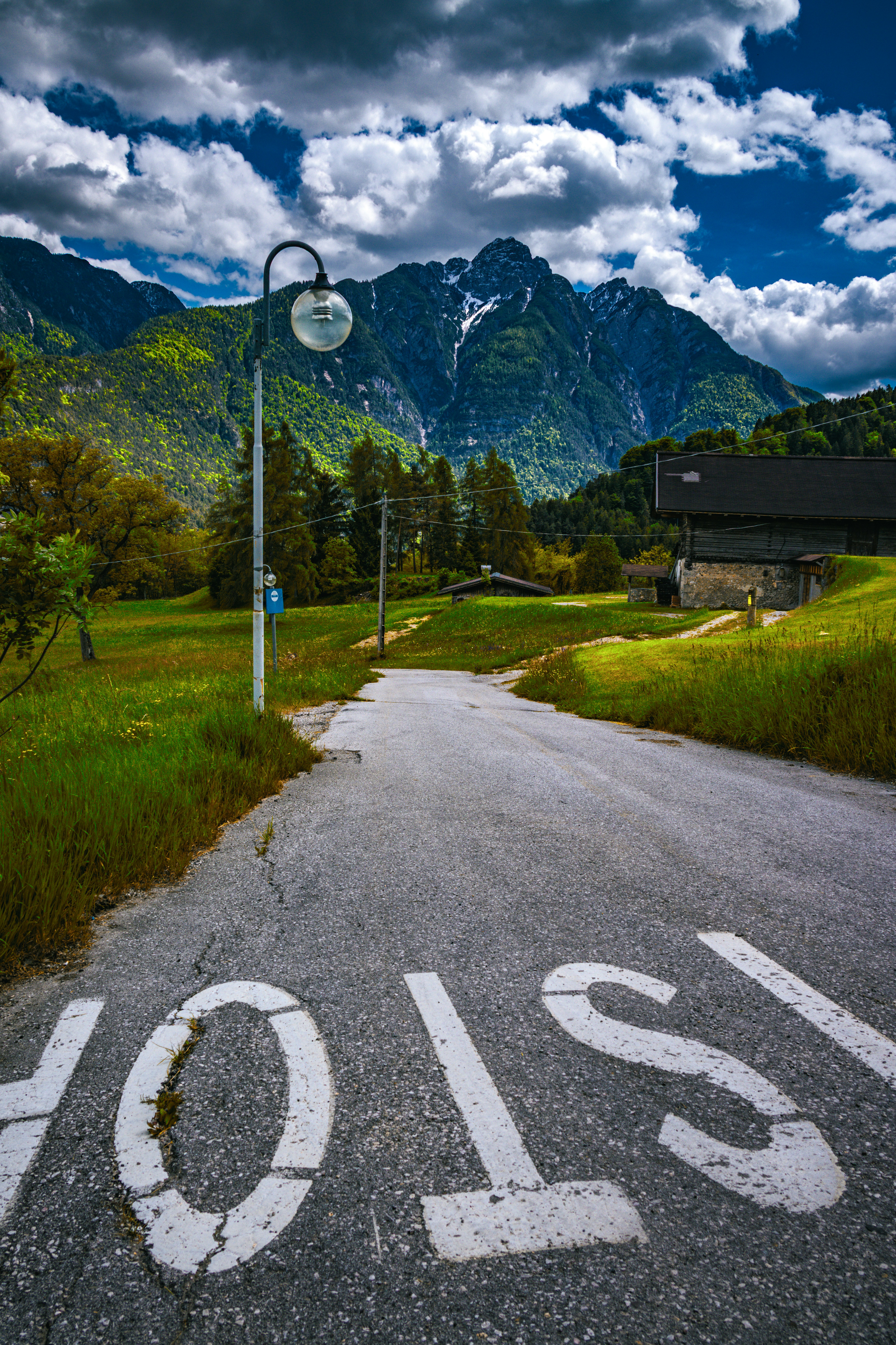 Rural Road Toward Craggy Peaks Under Dynamic Clouds