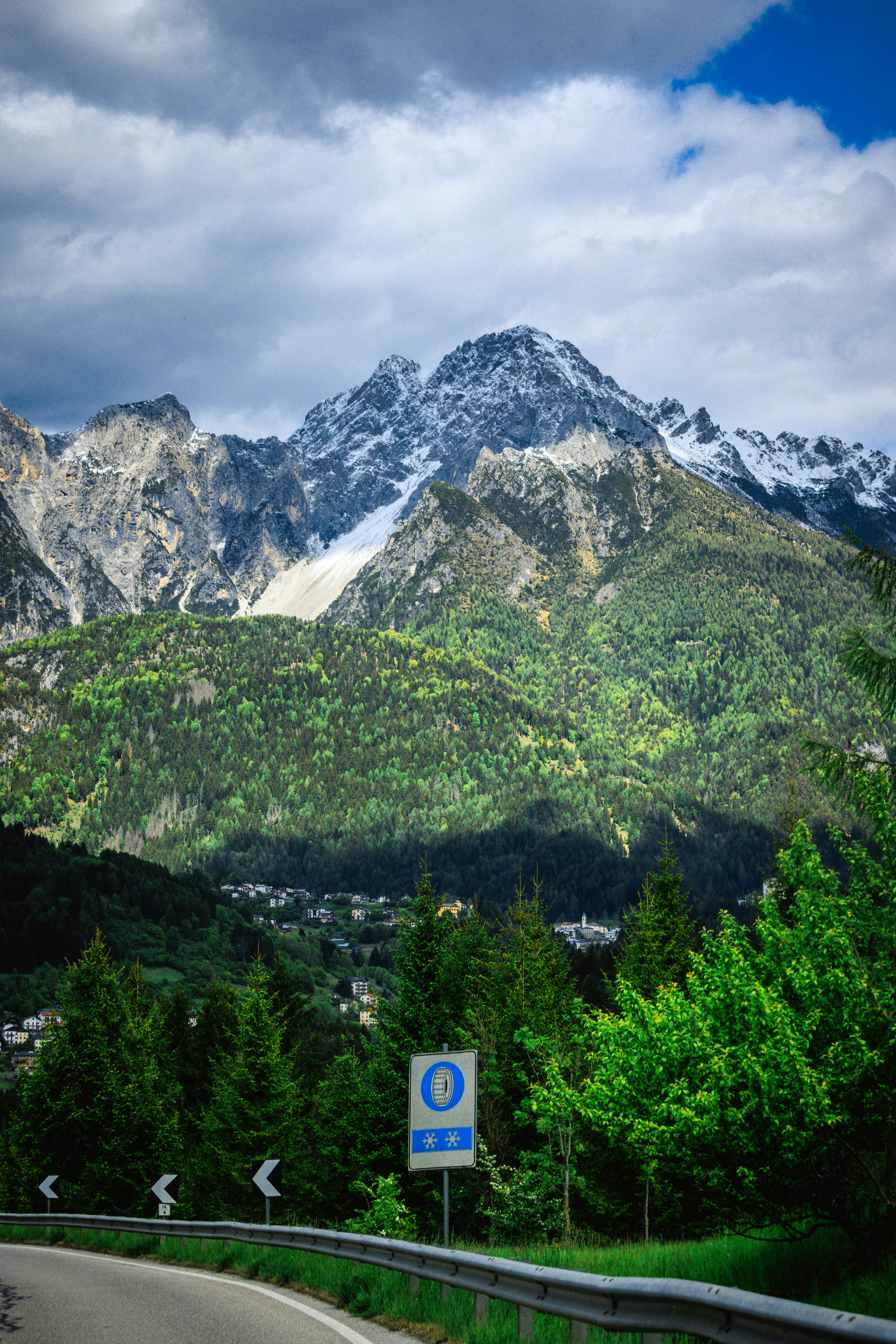 Snow-dusted peaks over a green valley with a winding road