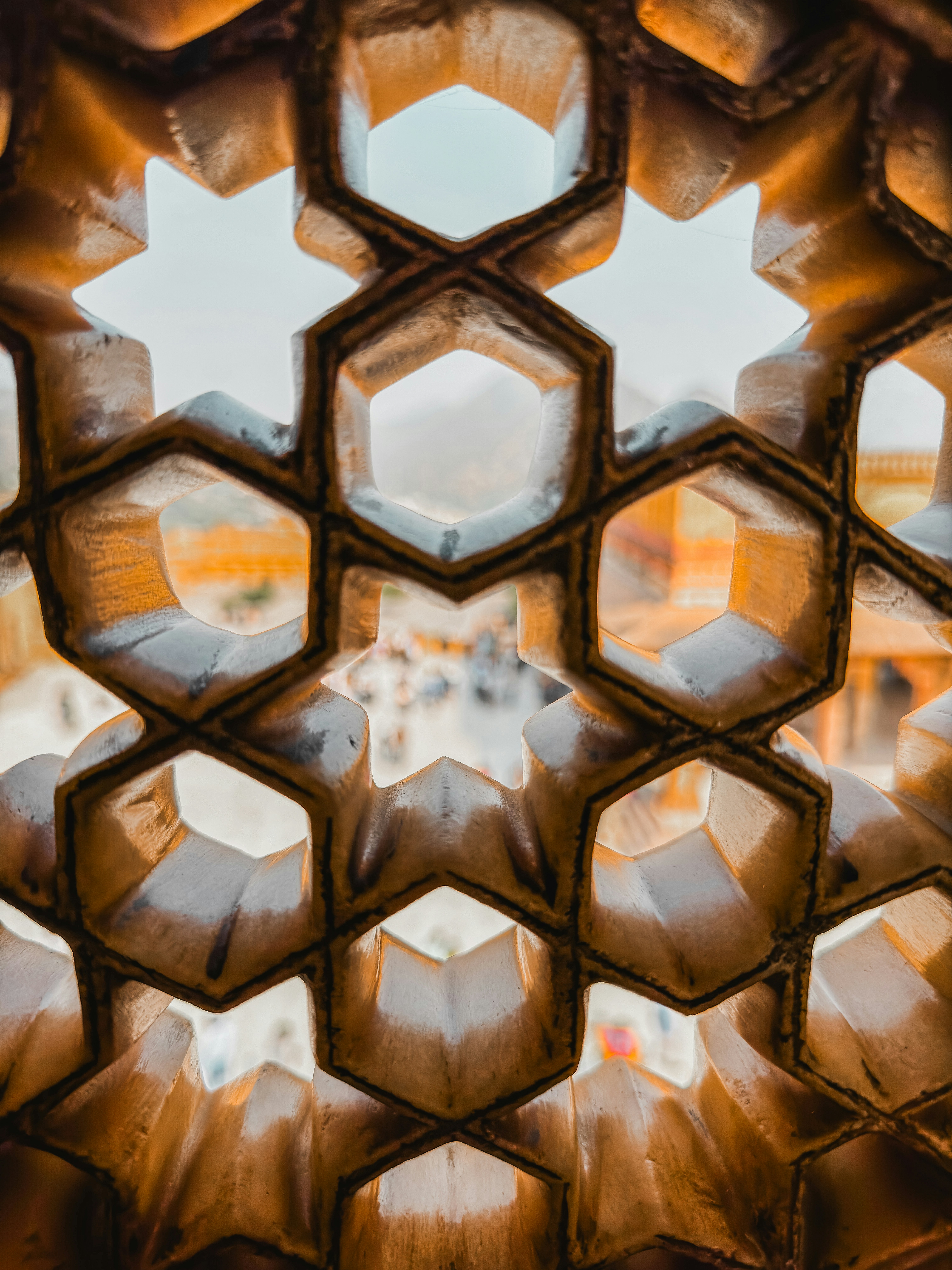 Close-up of a honeycomb-like lattice pattern with warm stone tones and a blurred courtyard beyond.