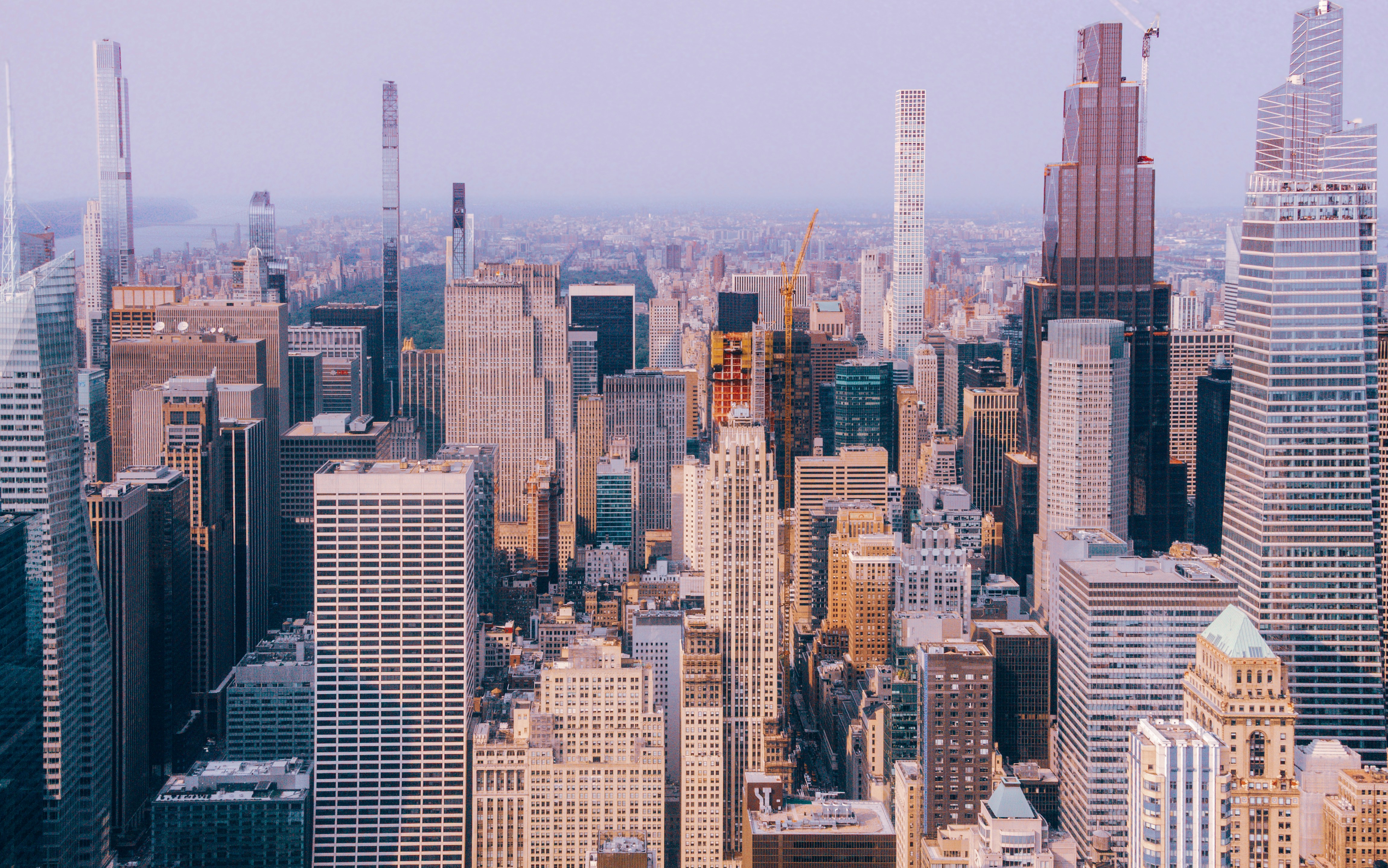 A dense urban skyline bathed in warm evening light, showcasing a mix of towering glass and brick facades.