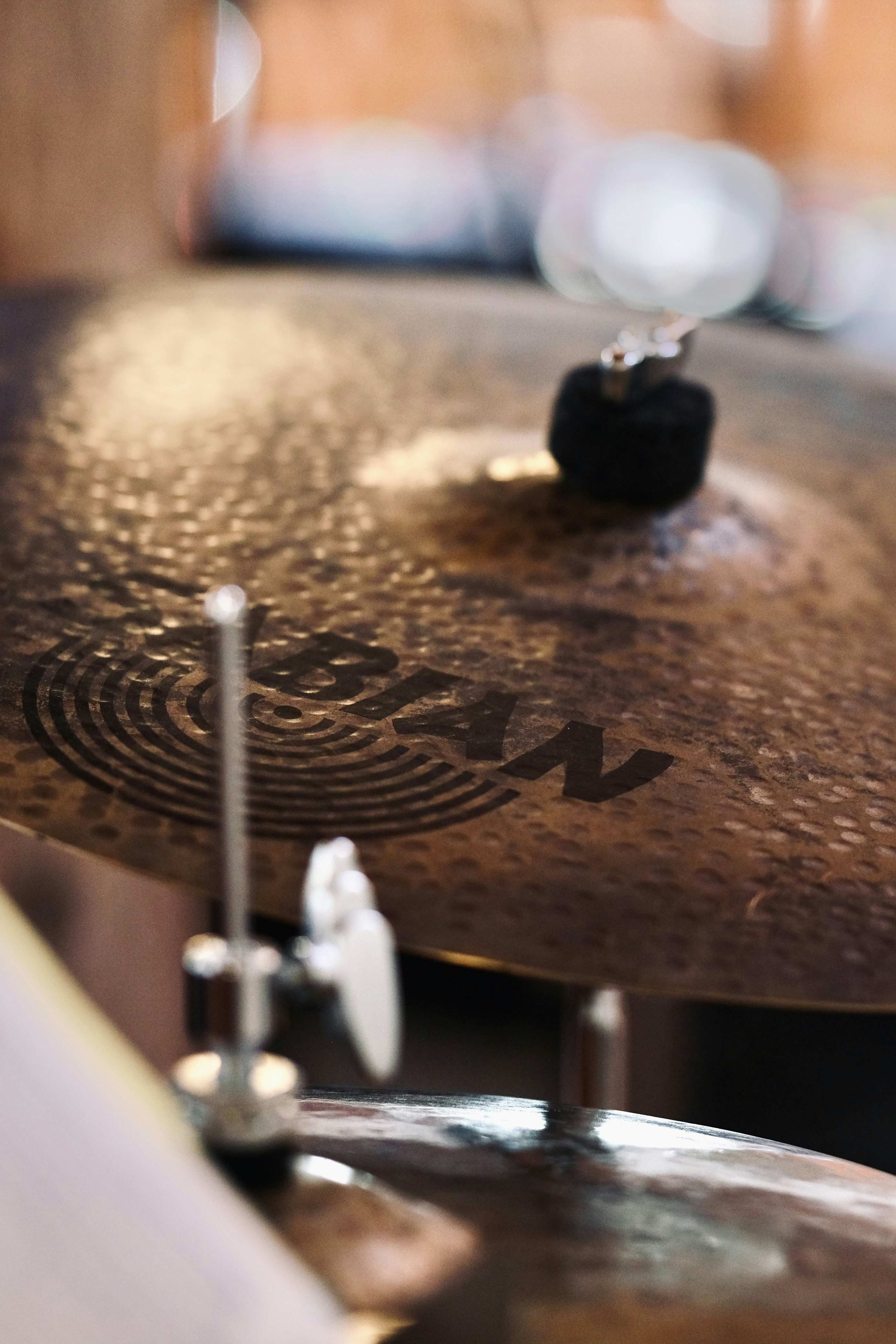 Close-up of a weathered cymbal with a focused central nub and a blurred kit in the background