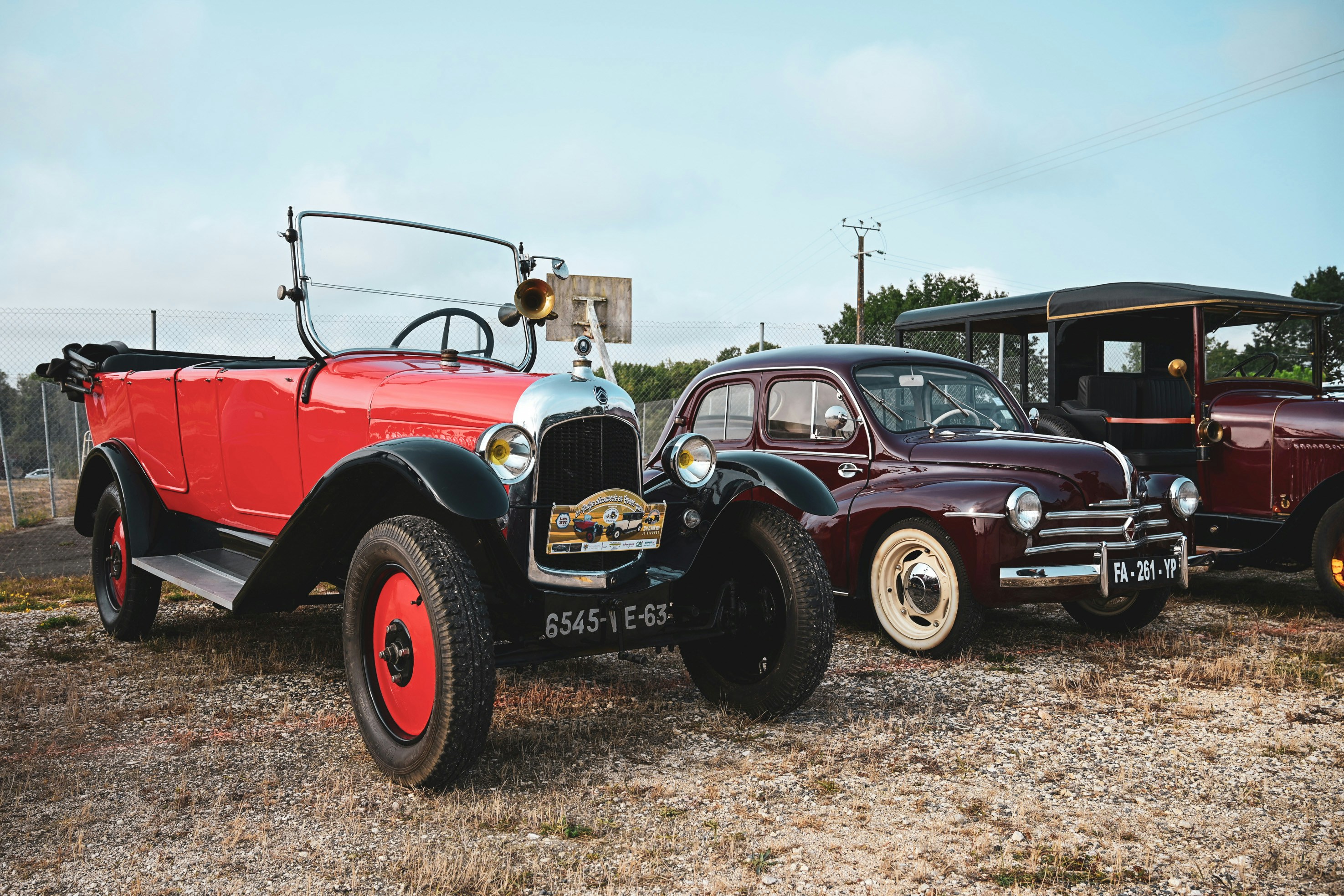 Red Vintage Convertible Leads a Row of Classic Cars in a Sunlit Field