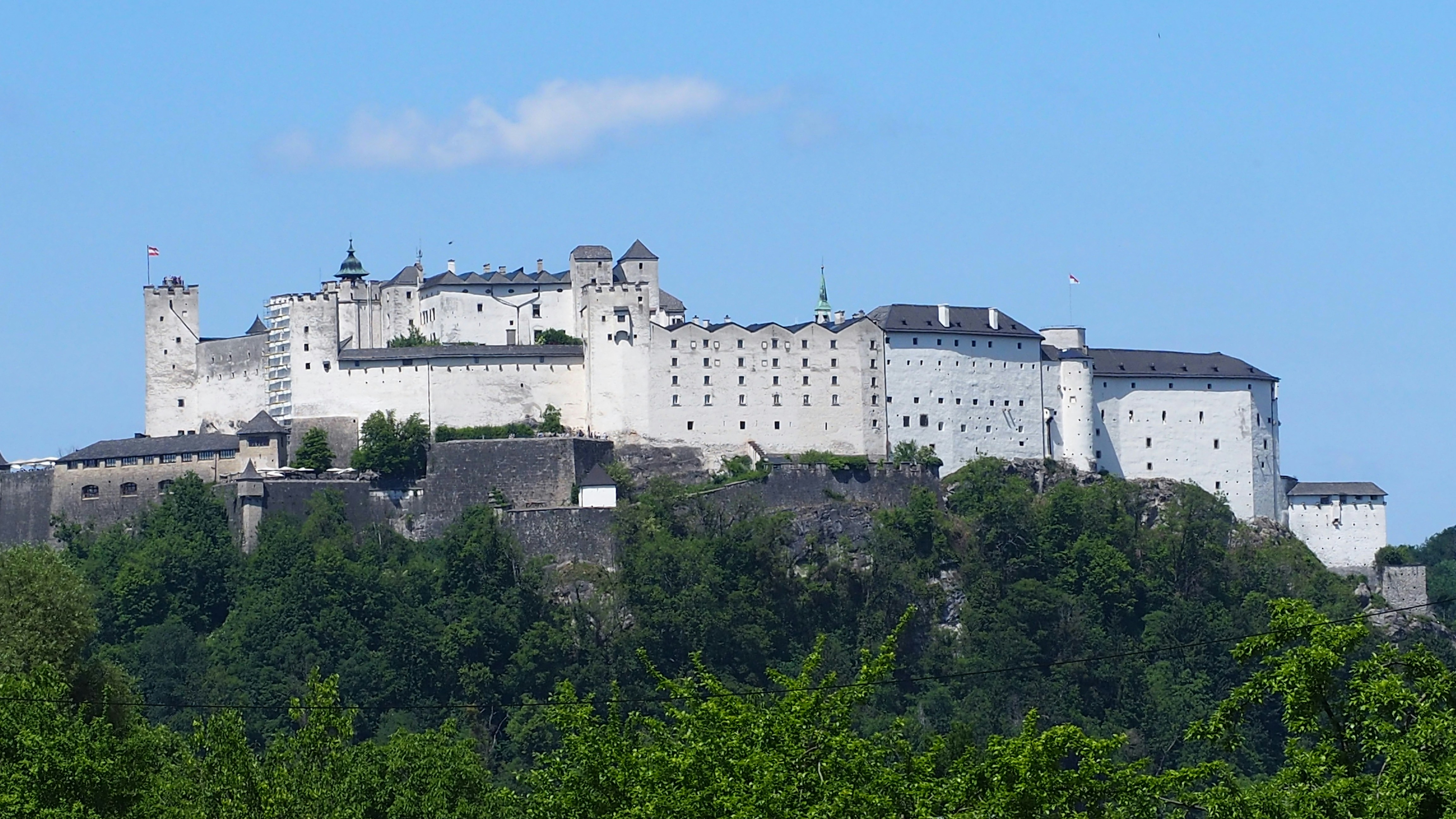 A expansive fortress sits atop a green hillside under a clear blue sky, its white stone walls dominating the landscape.