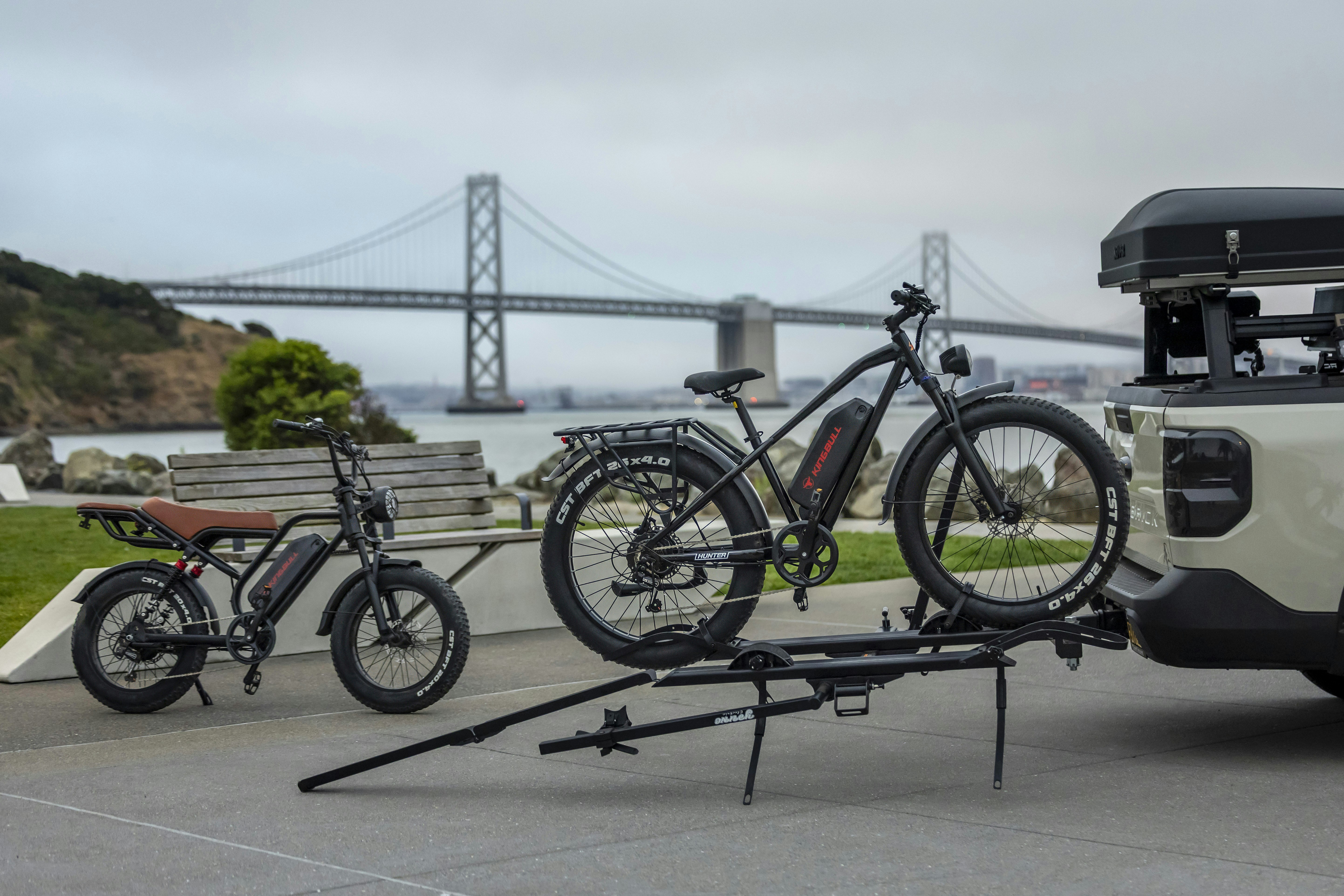 Two e-bikes on a trailer setup near a scenic bridge overlook