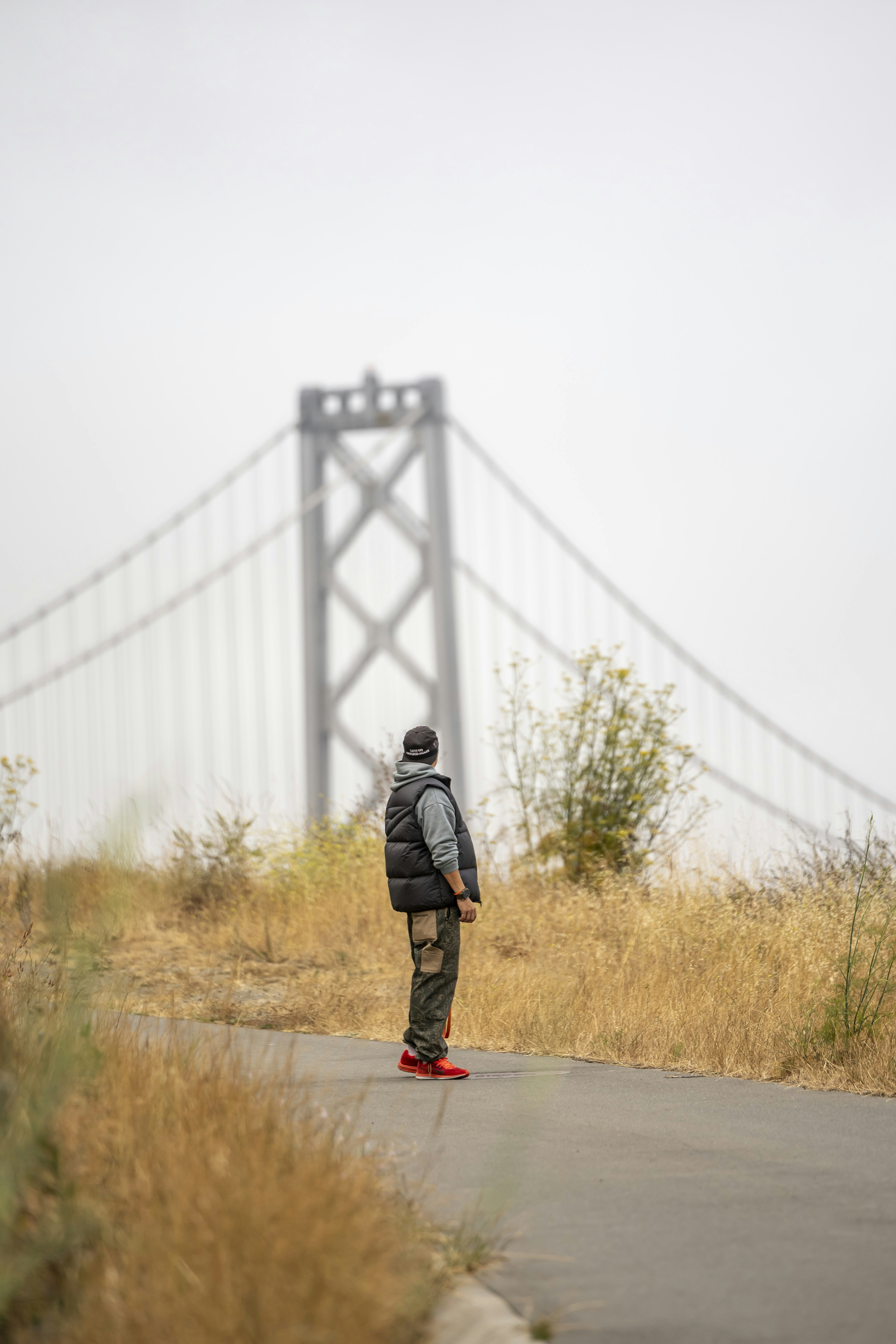 Man stands on path, viewing a bridge in the fog.