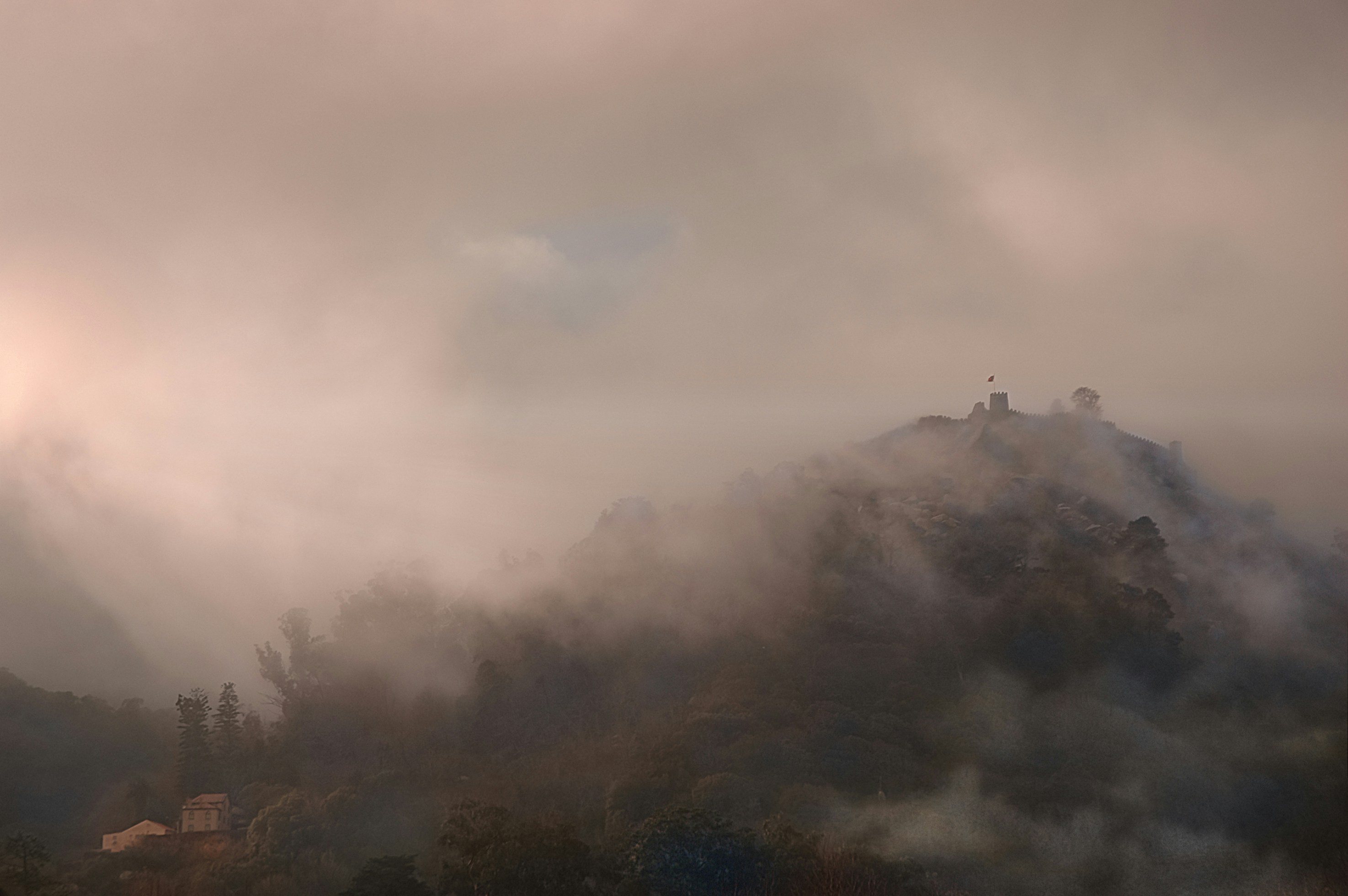 Misty Summit: A Watchful Peak Emerges from Soft Dawn Clouds
