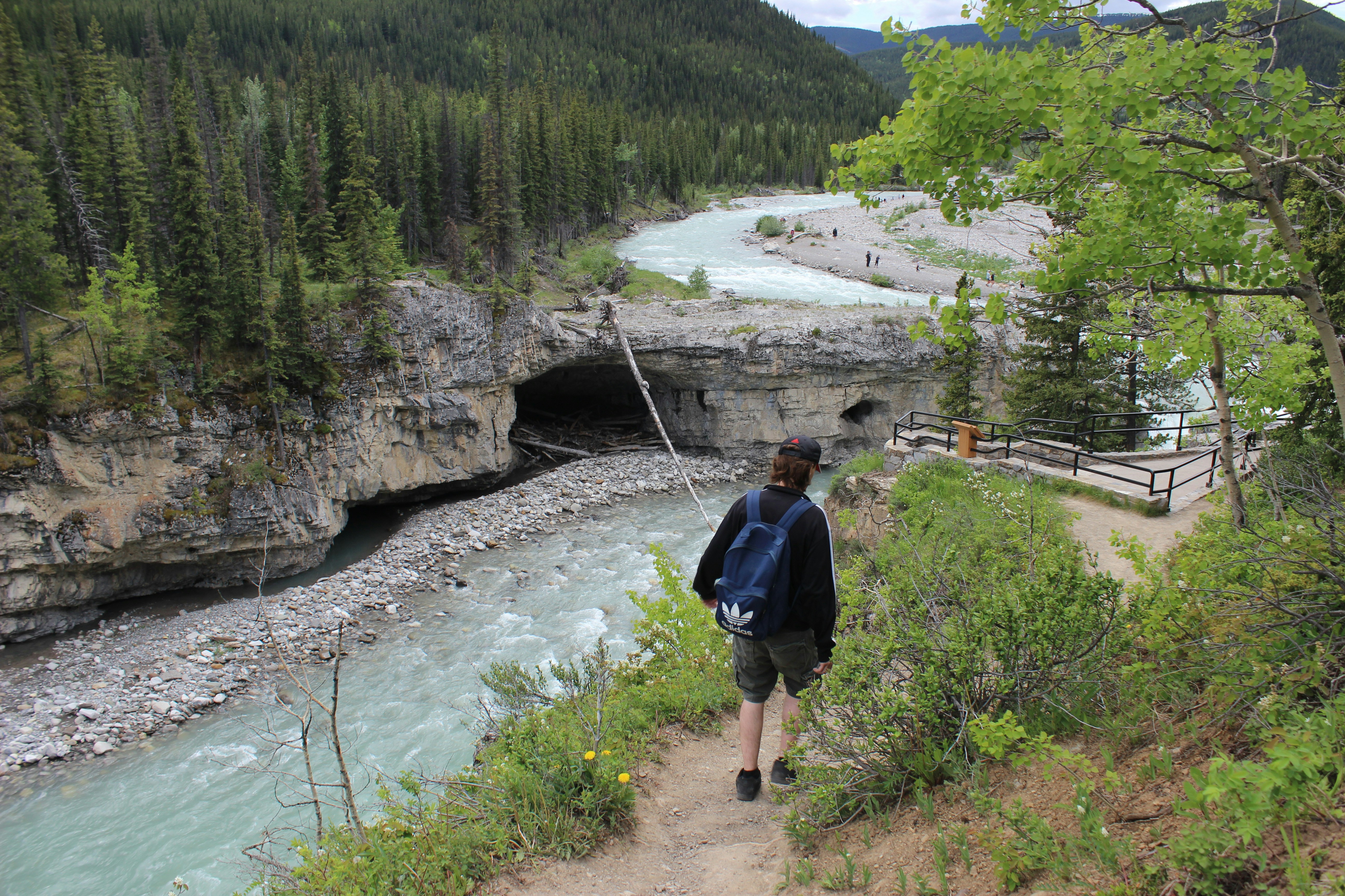 Hiker on a cliffside trail overlooking a turquoise river valley