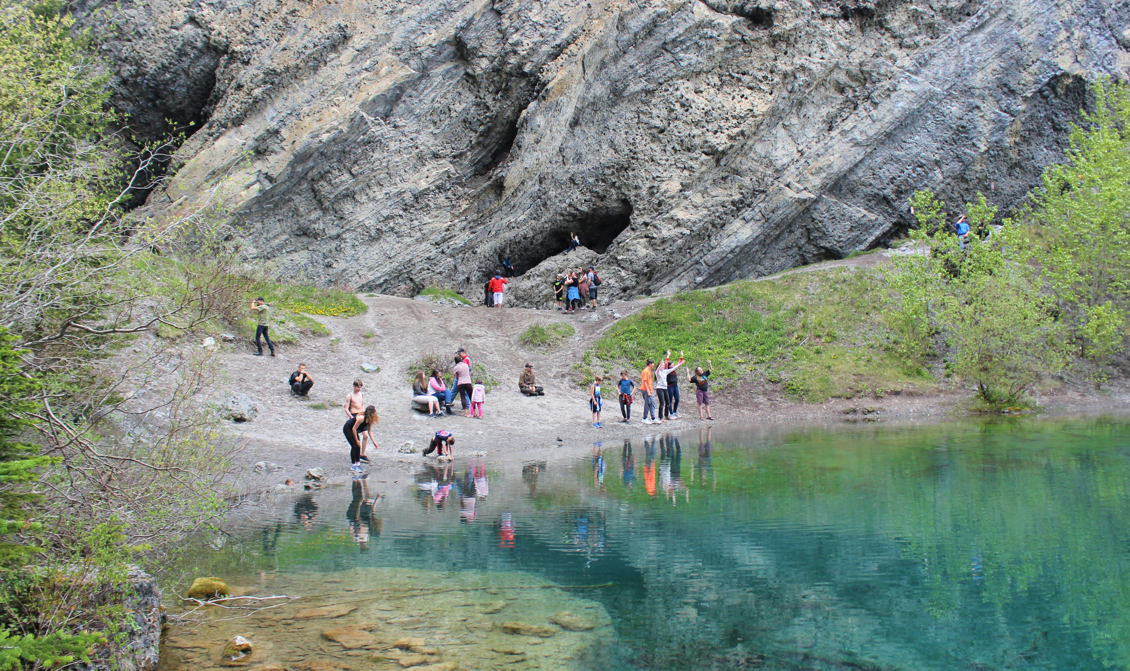 People by the turquoise pool: exploring a rocky lakeshore cave
