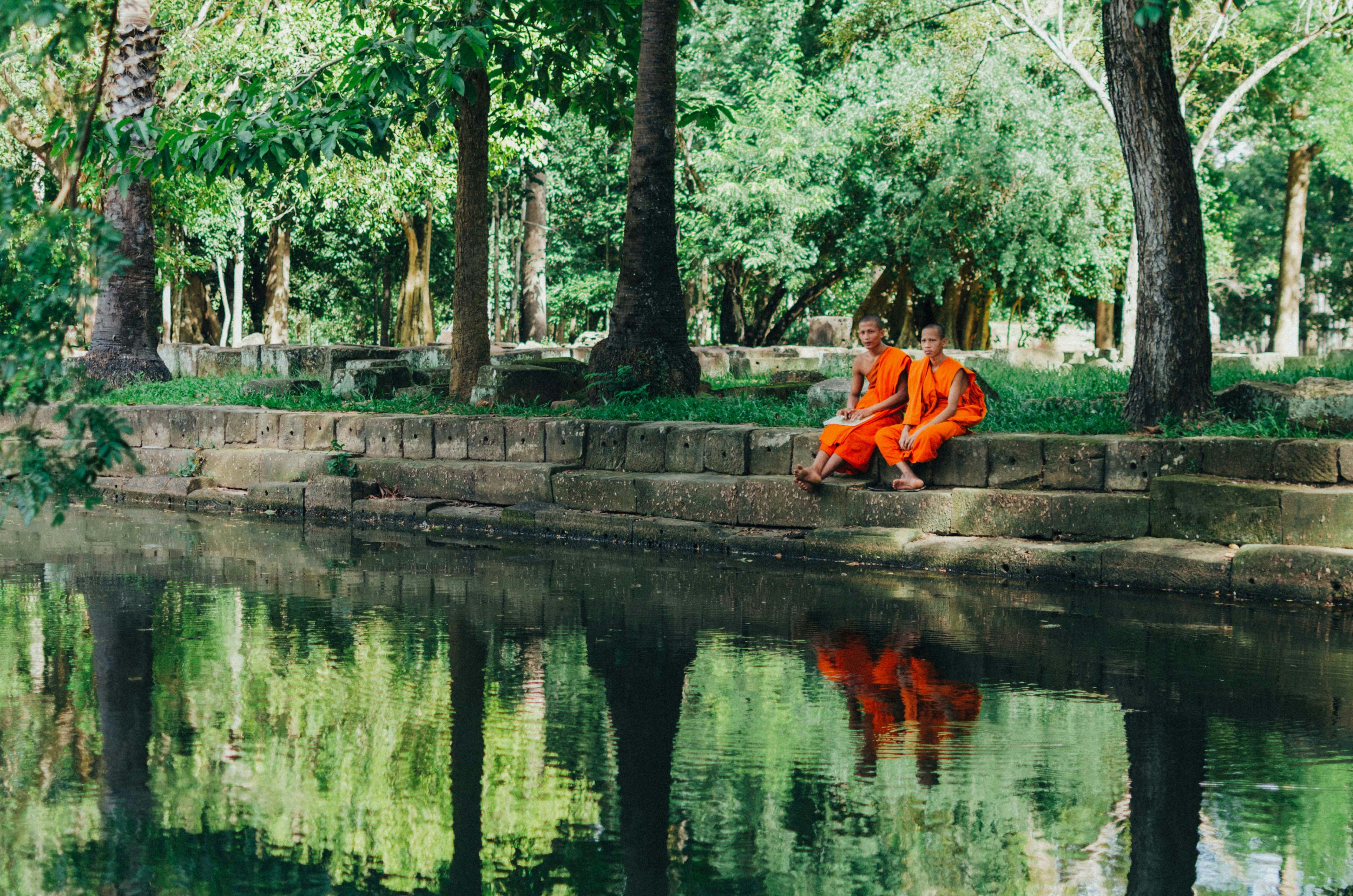 Two orange-robed figures by a tranquil canal reflect their presence