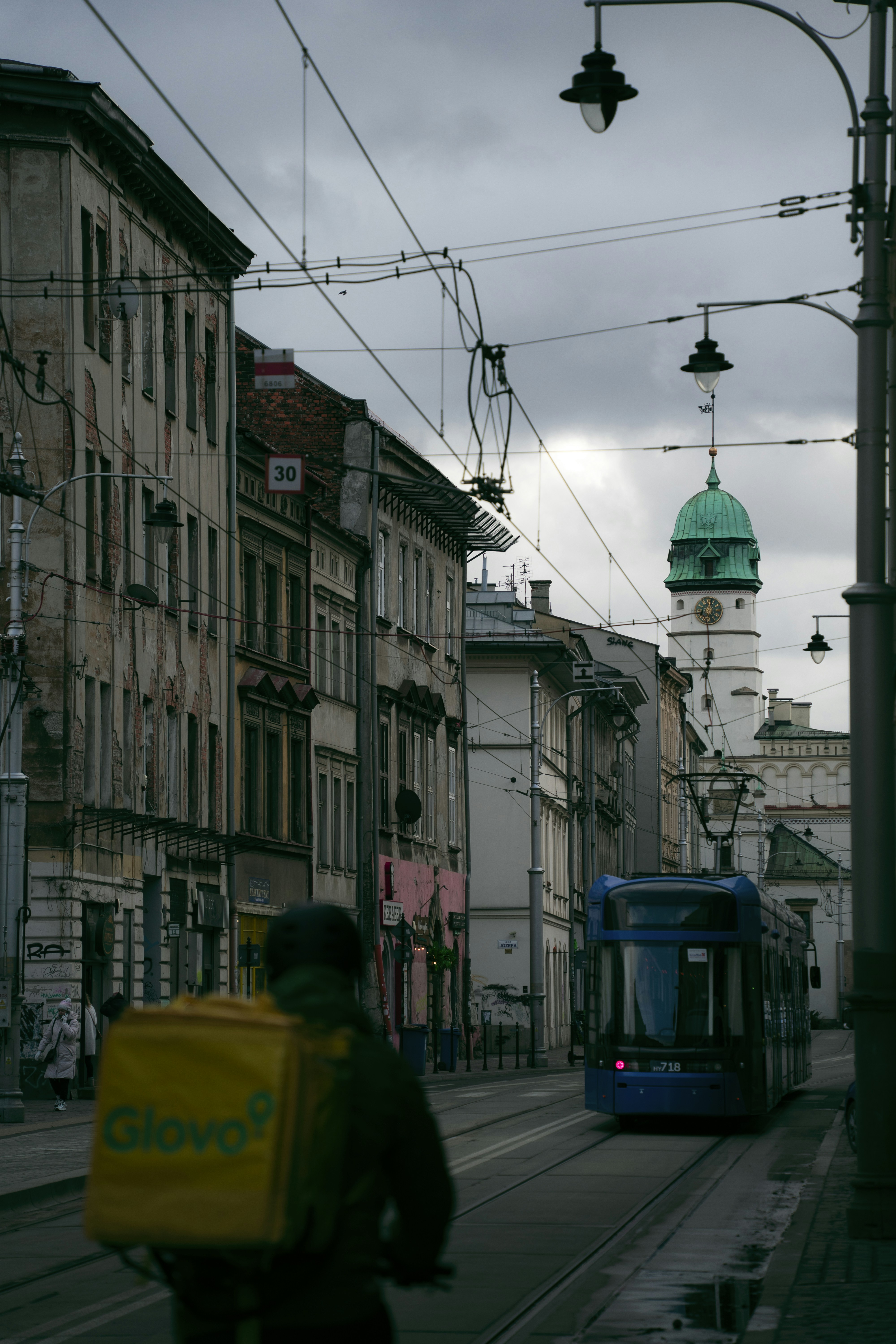 Glovo delivery person, blue tram, and historic city street.