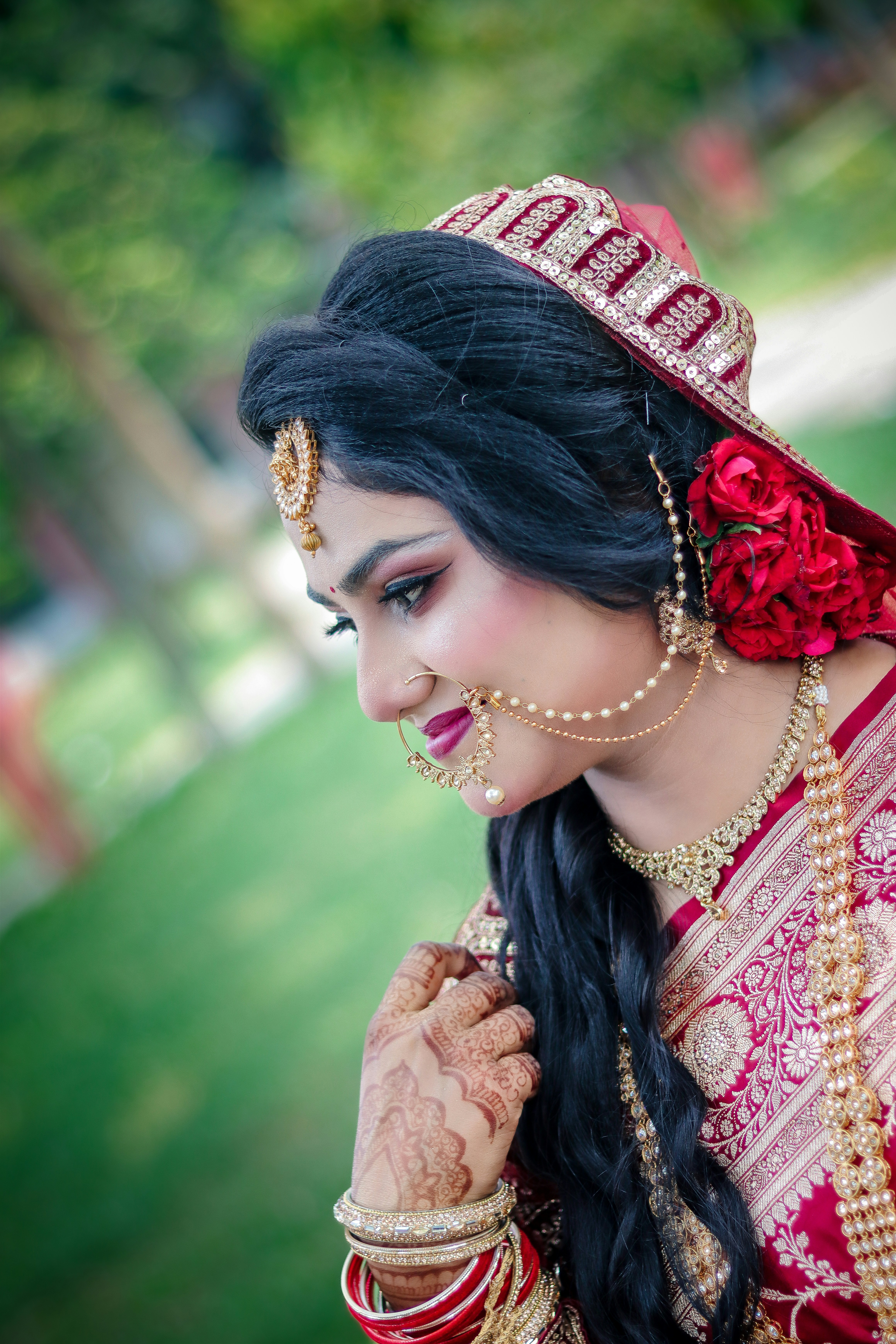 Bride in ornate red and gold attire with traditional jewelry, captured in profile during a garden shoot.