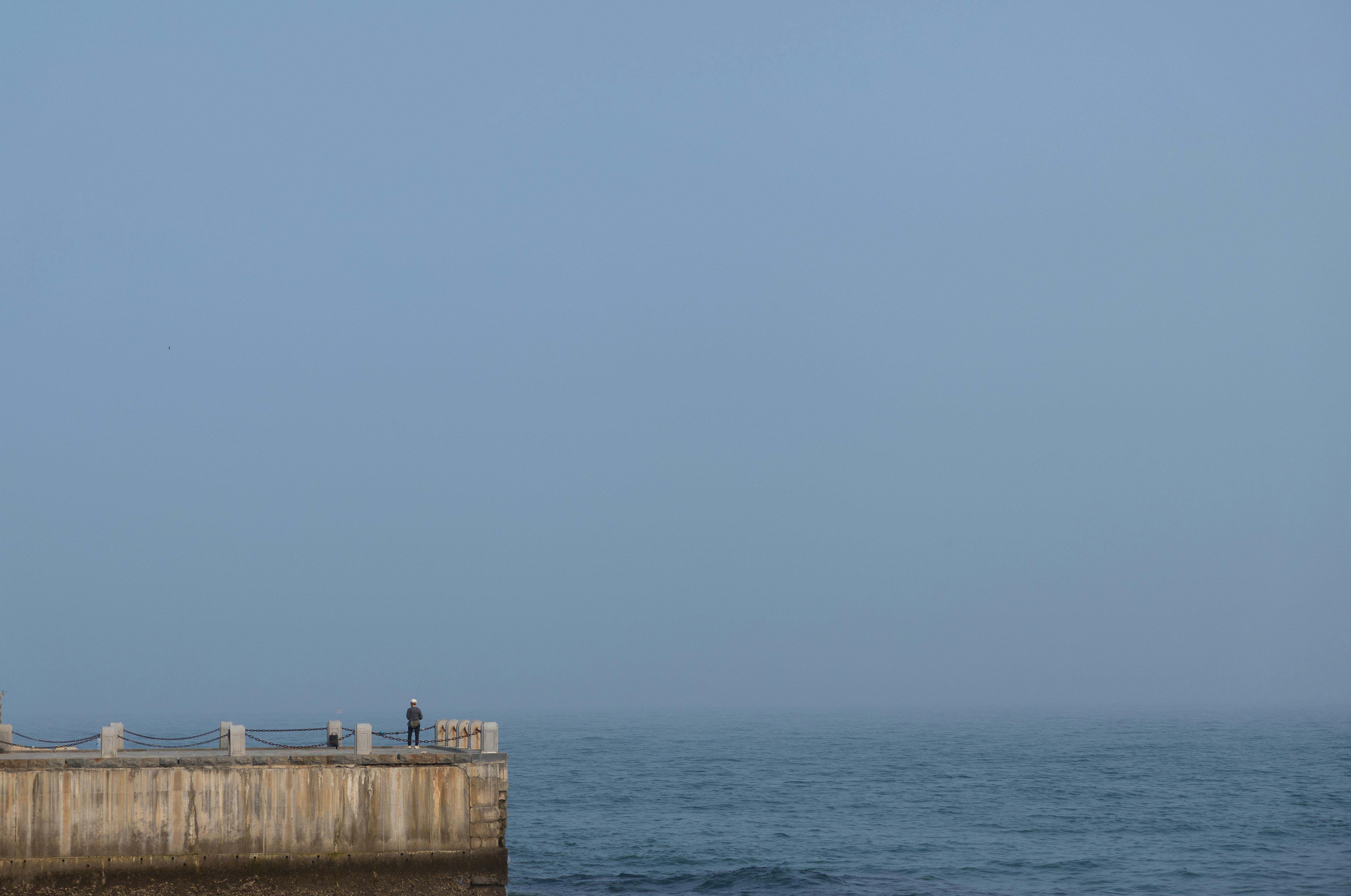  lone figure at the edge of a quiet pier over a calm sea