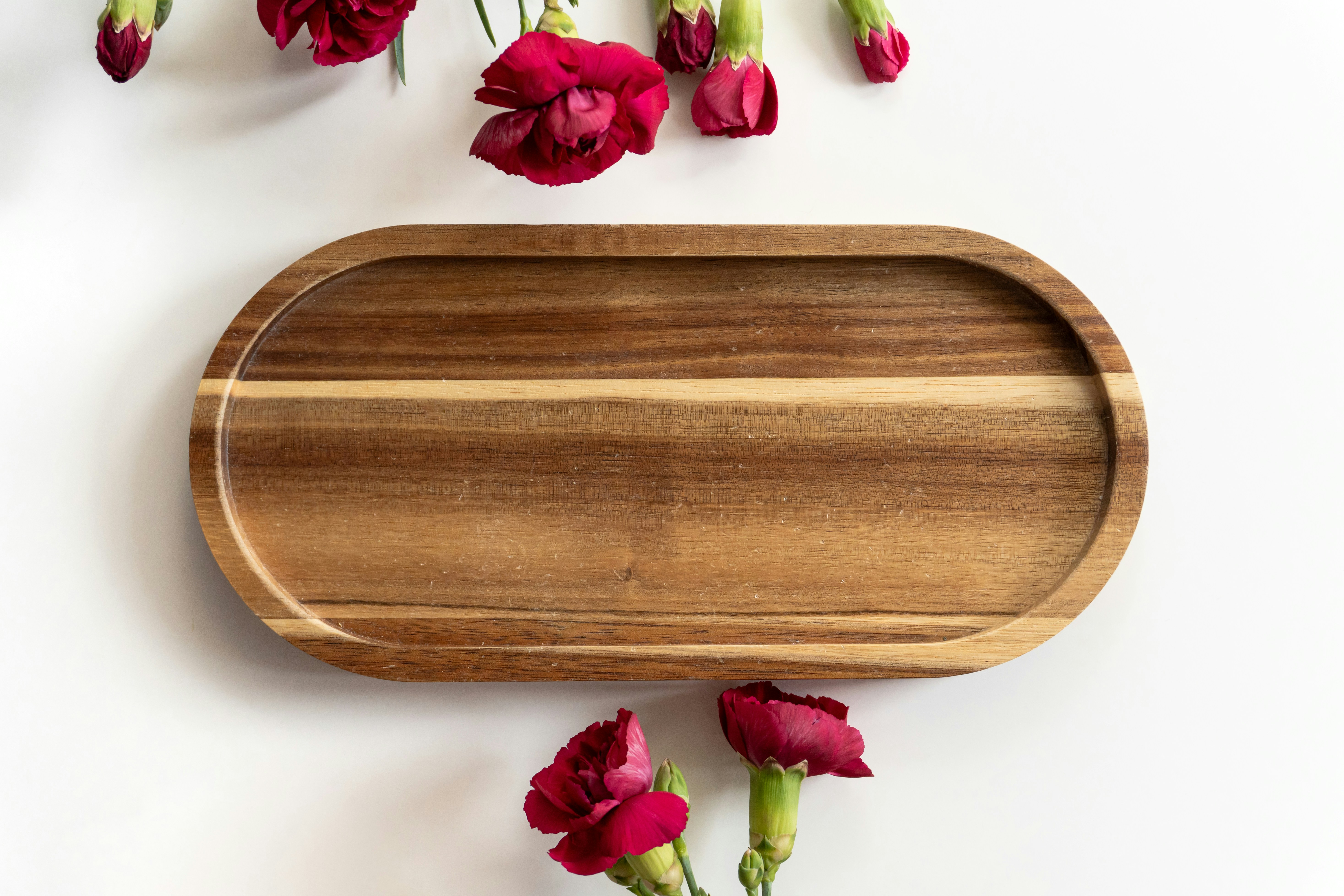 Wooden tray centered on a white canvas with pink carnations