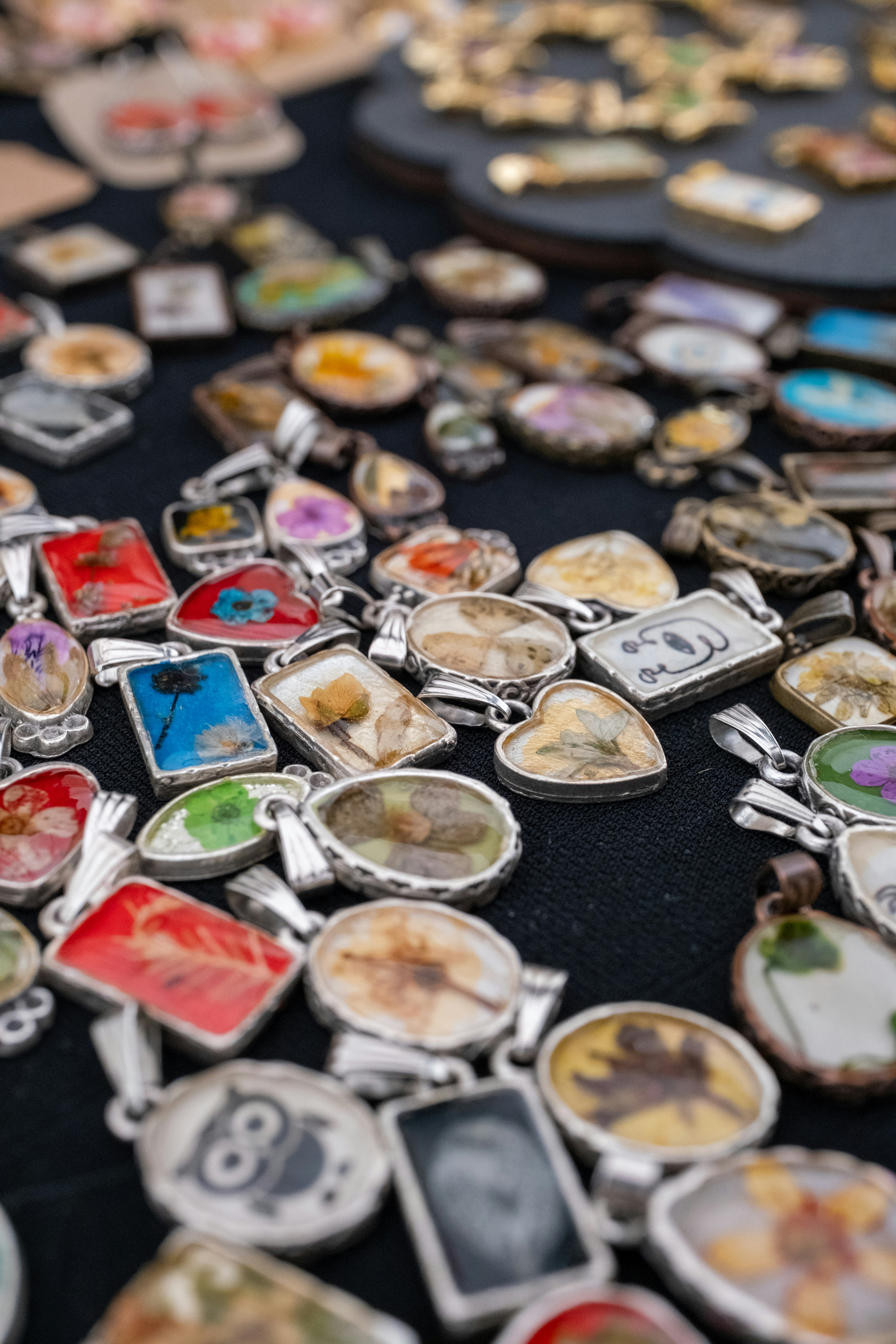 Small metal pendants and charms with colorful images lay scattered on dark fabric, hinting at a jewelry stall or craft decor setup.