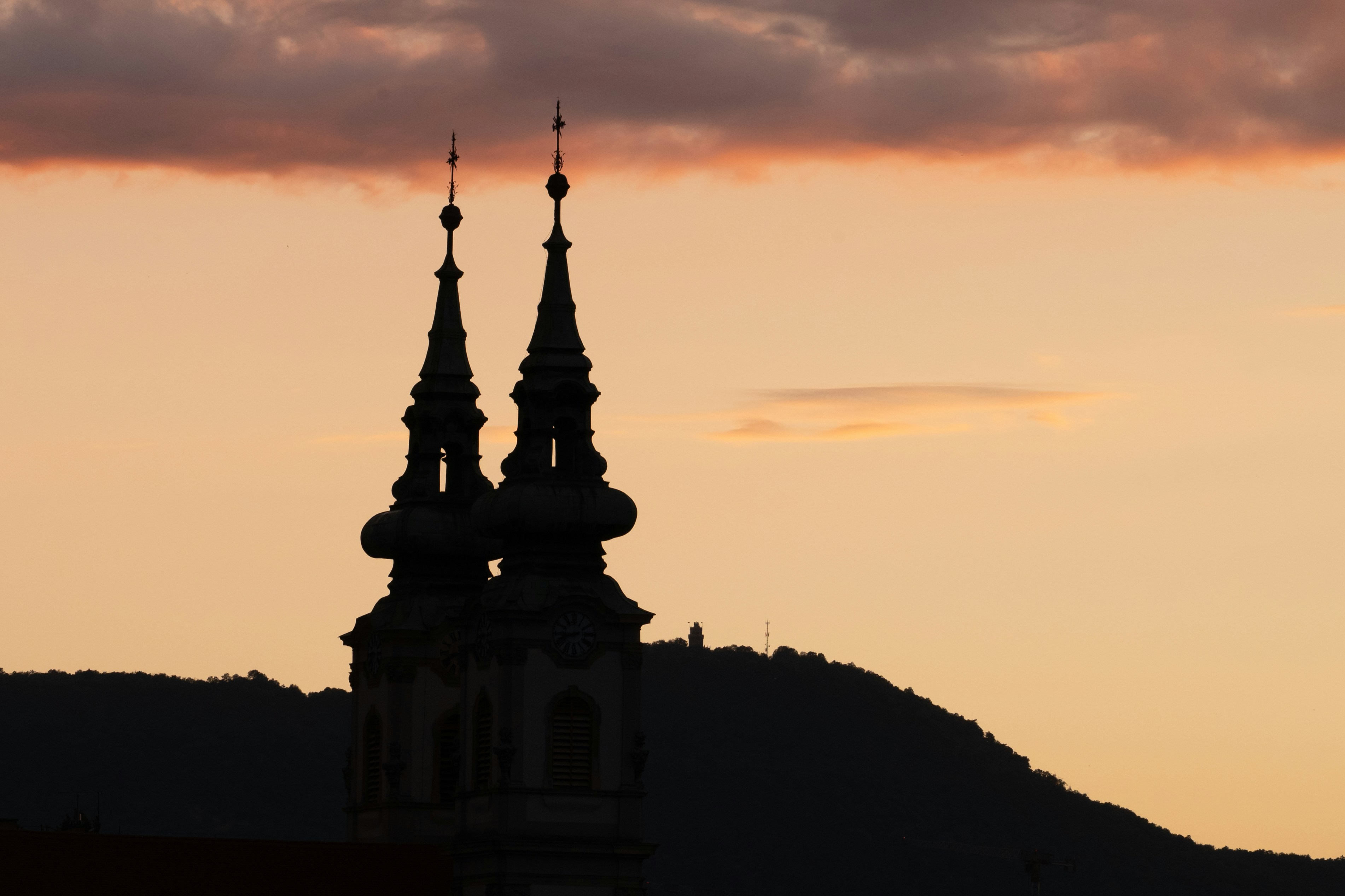 Silhouetted church spires and hill against a colorful sunset sky.