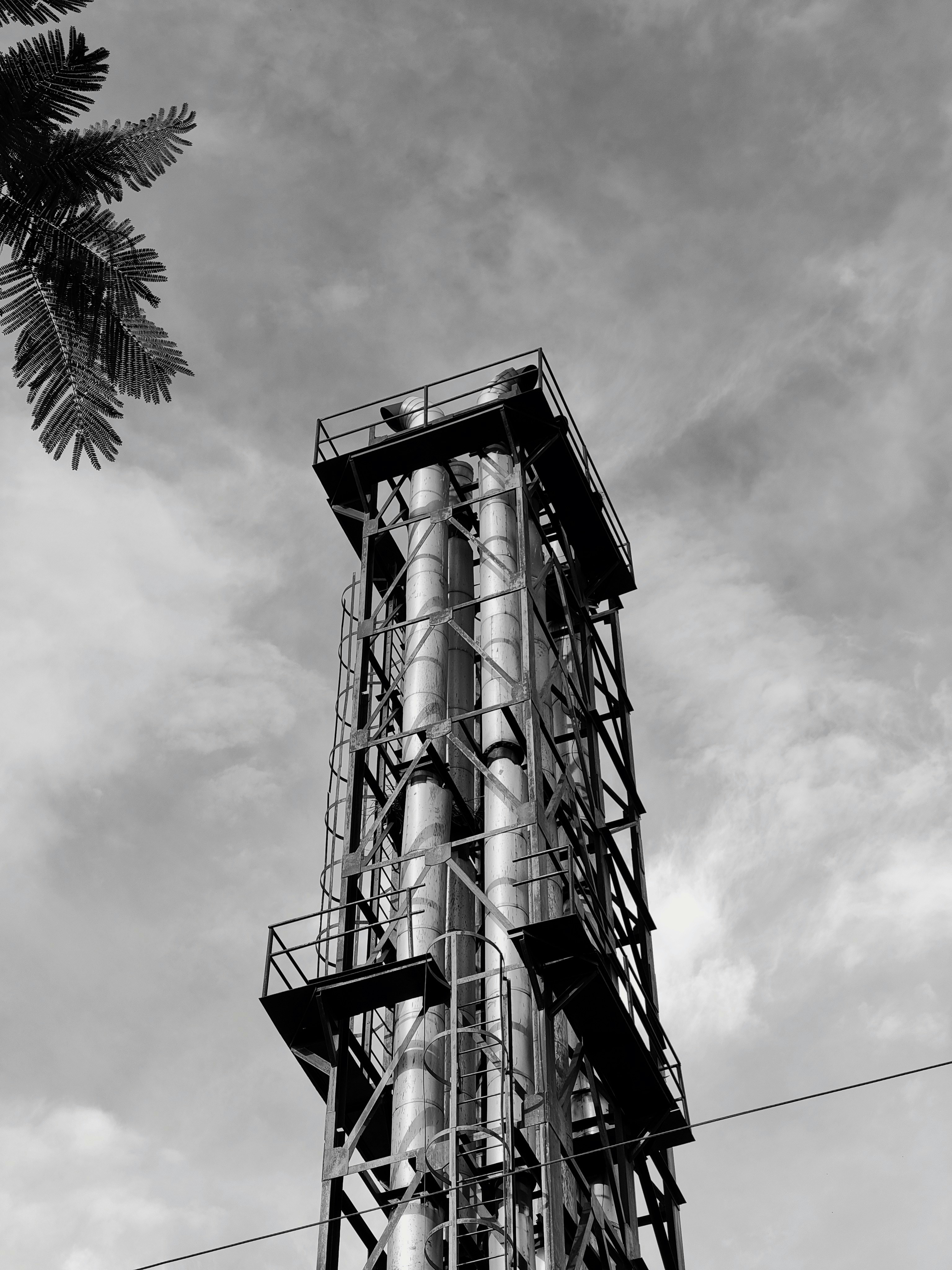 Industrial metal structure rising against a cloudy sky, captured in black and white to emphasize form and texture.