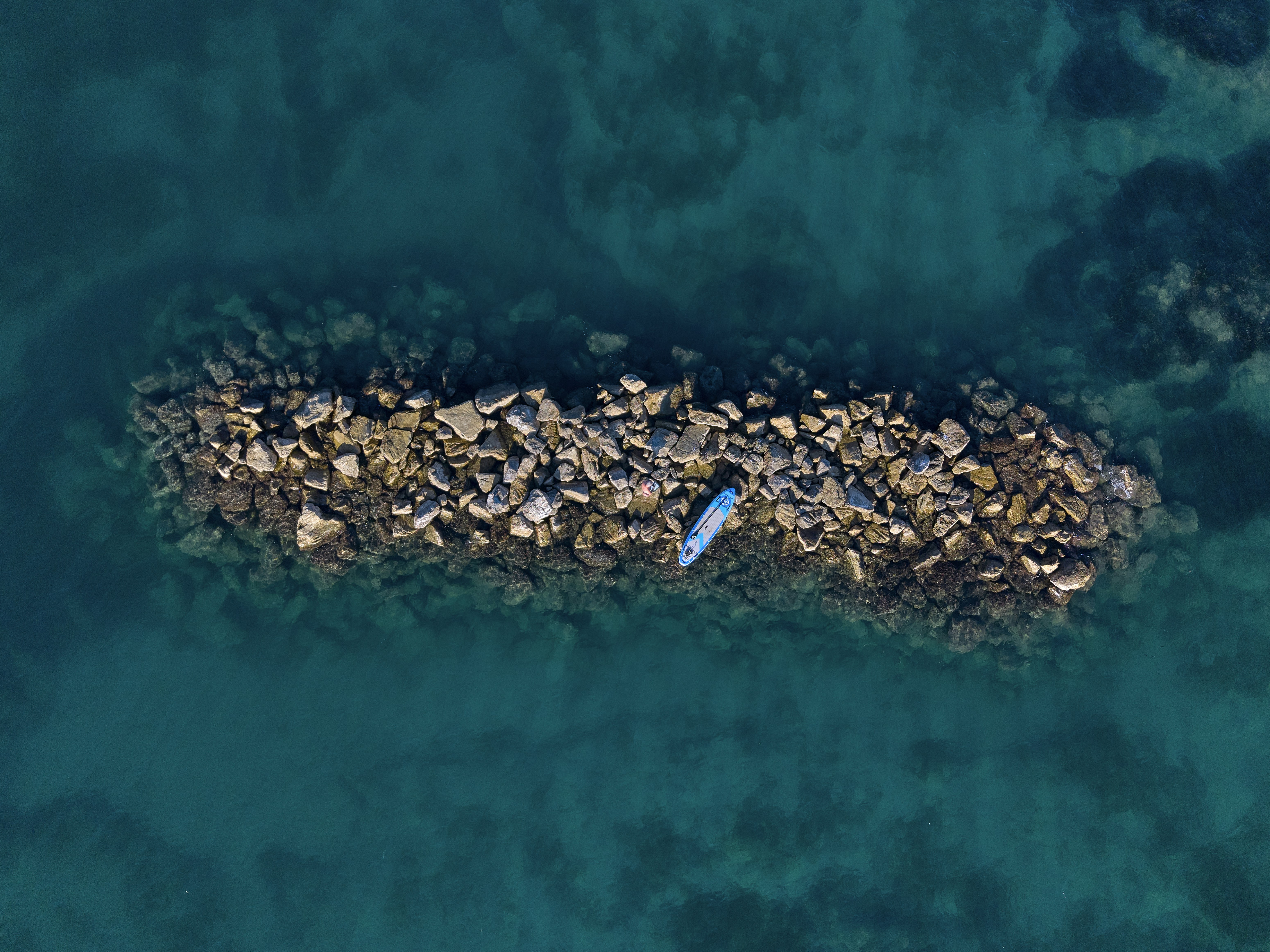 Blue Boat Resting on a Rock Breakwater in Turquoise Waters