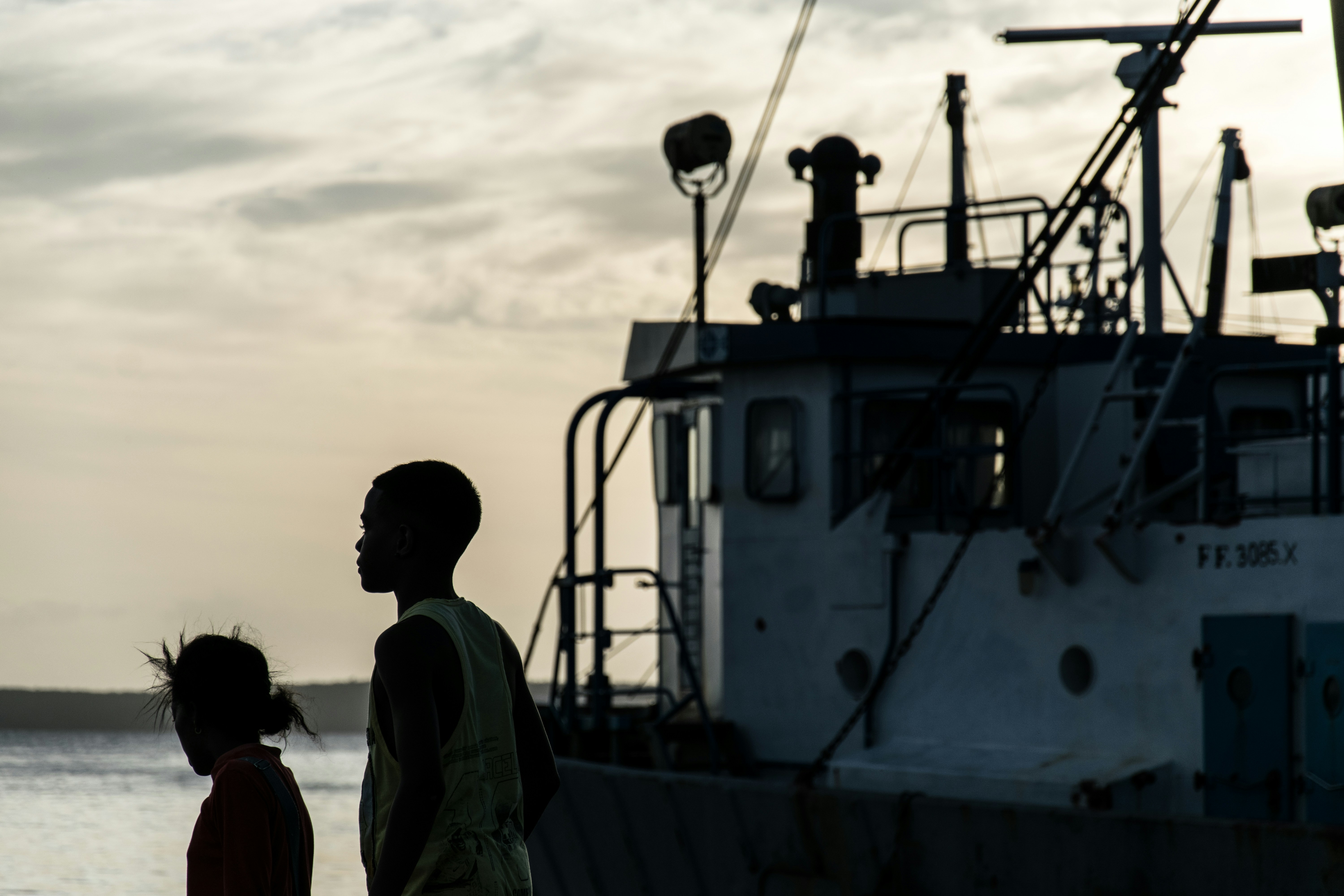 Silhouetted Harbor Life: Children in the Gentle Dusk by the Docked Vessel