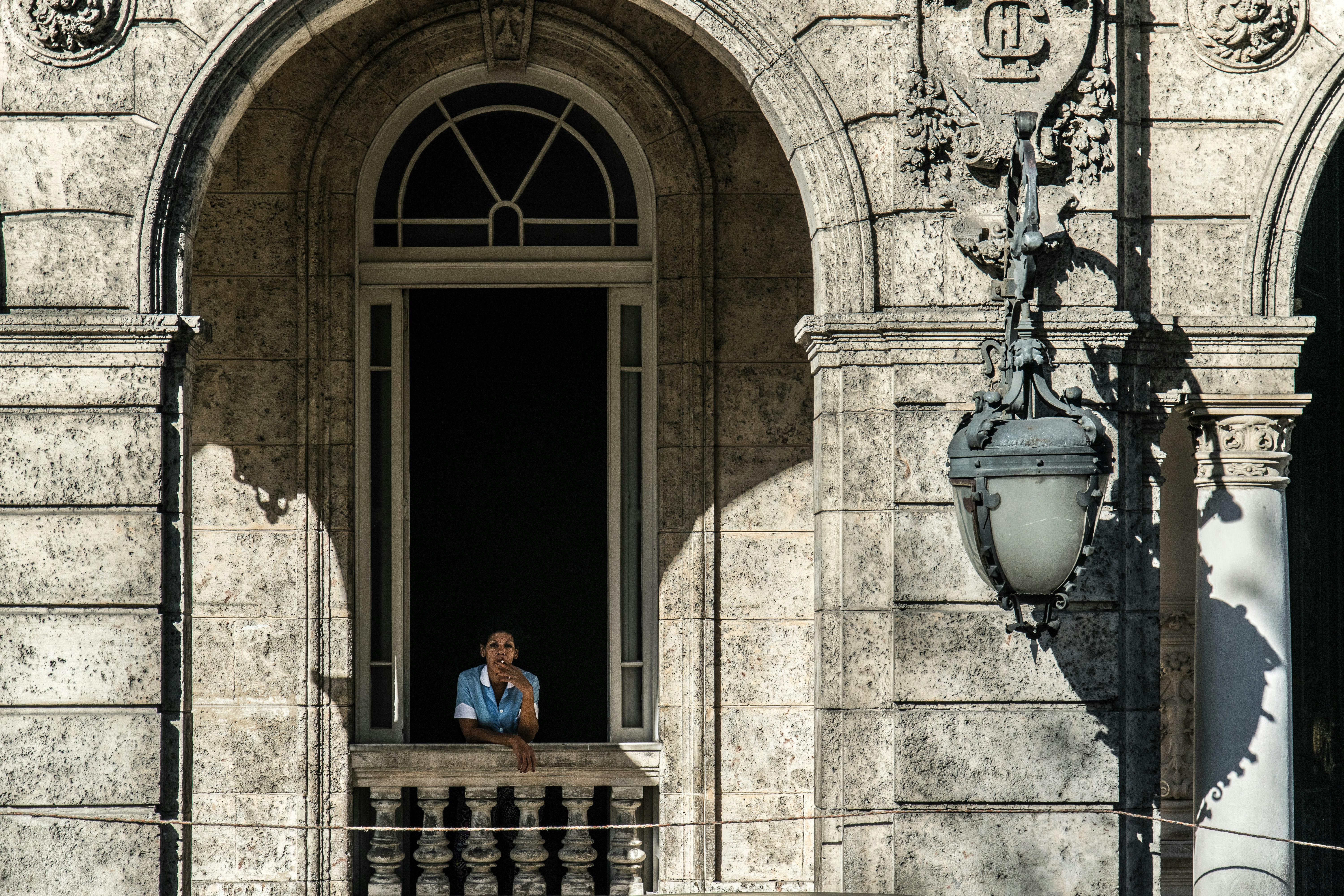 Balcony Quiet: A solitary figure rests in a sunlit archway