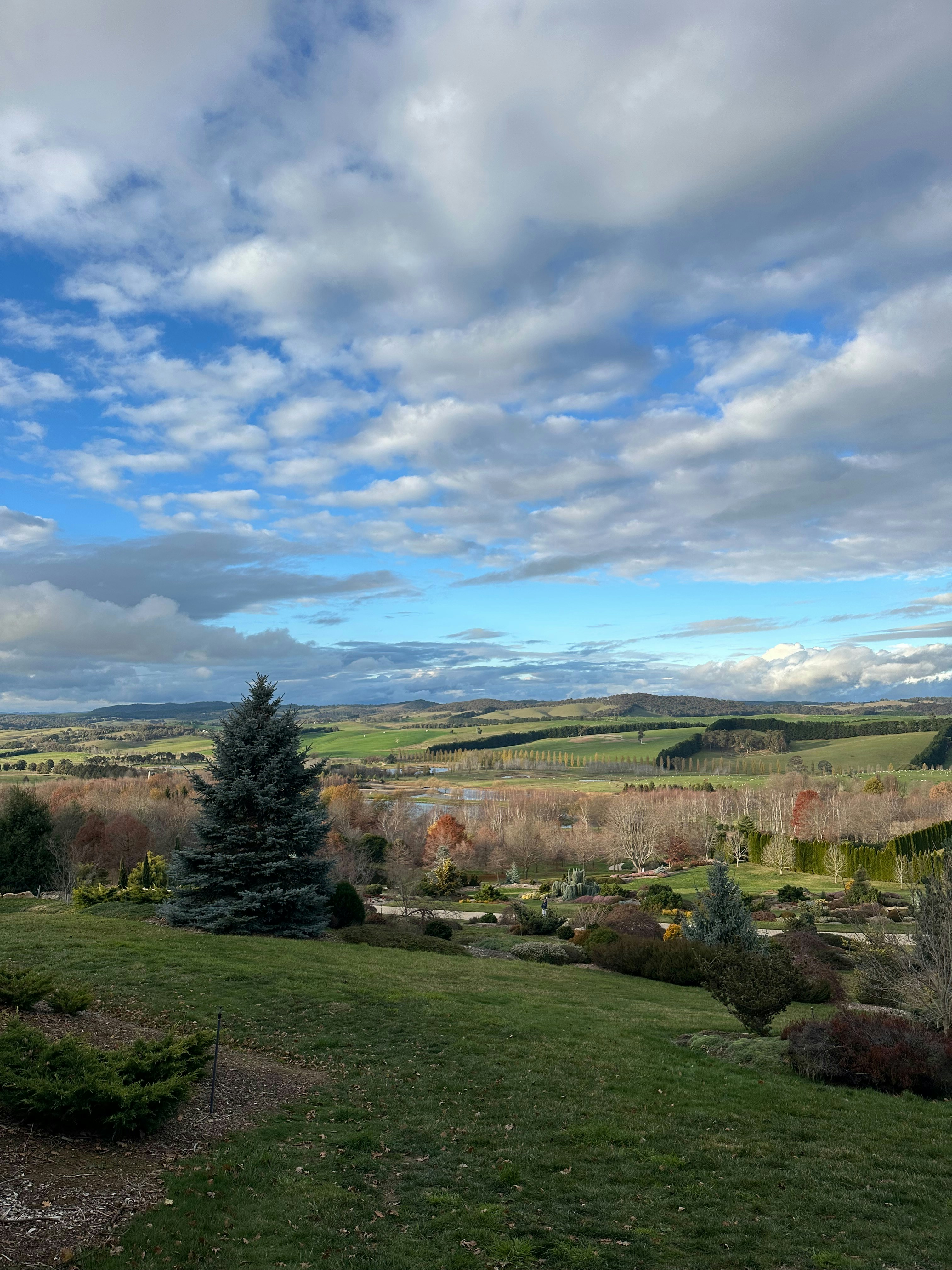 Patchwork farmland and a manicured garden roll toward distant hills beneath a bright, partly cloudy sky.